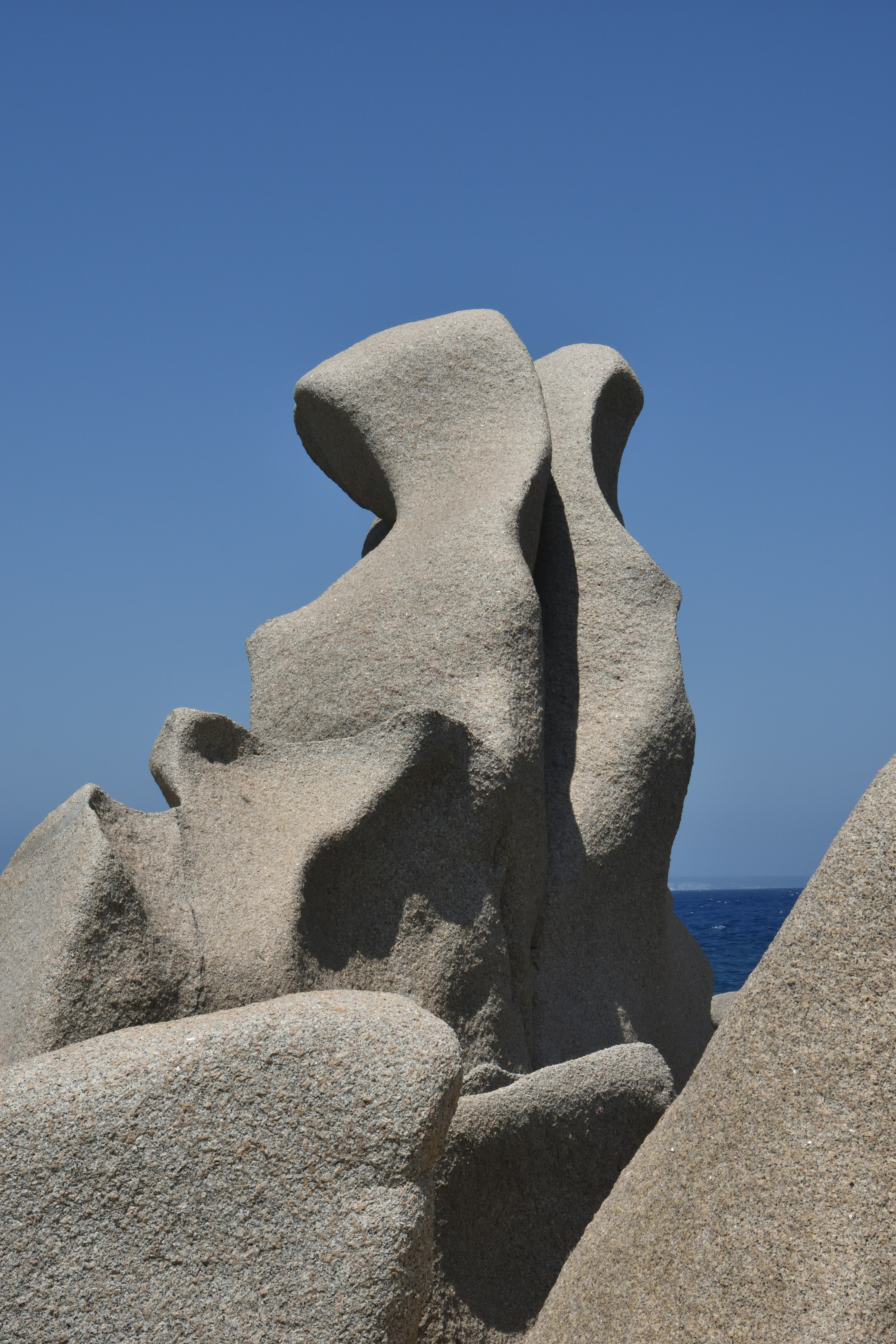 Abstract rock formation resembling human figures against a clear blue sky, highlighting the interplay between natural elements and artistic perception.