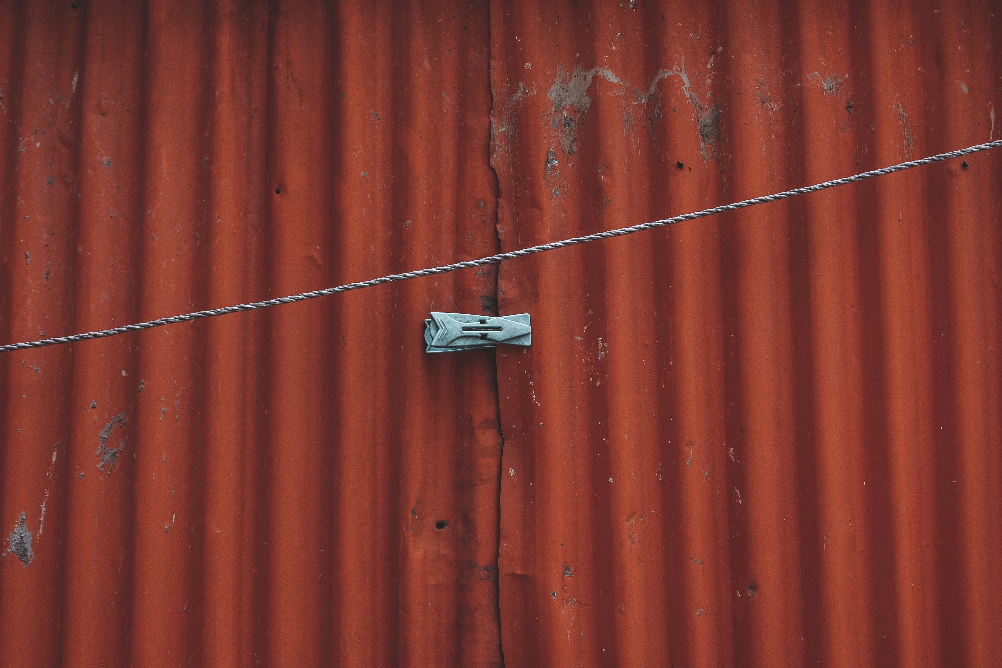 Blue Clip Anchoring a Slanted Wire Across Weathered Red Corrugated Steel
