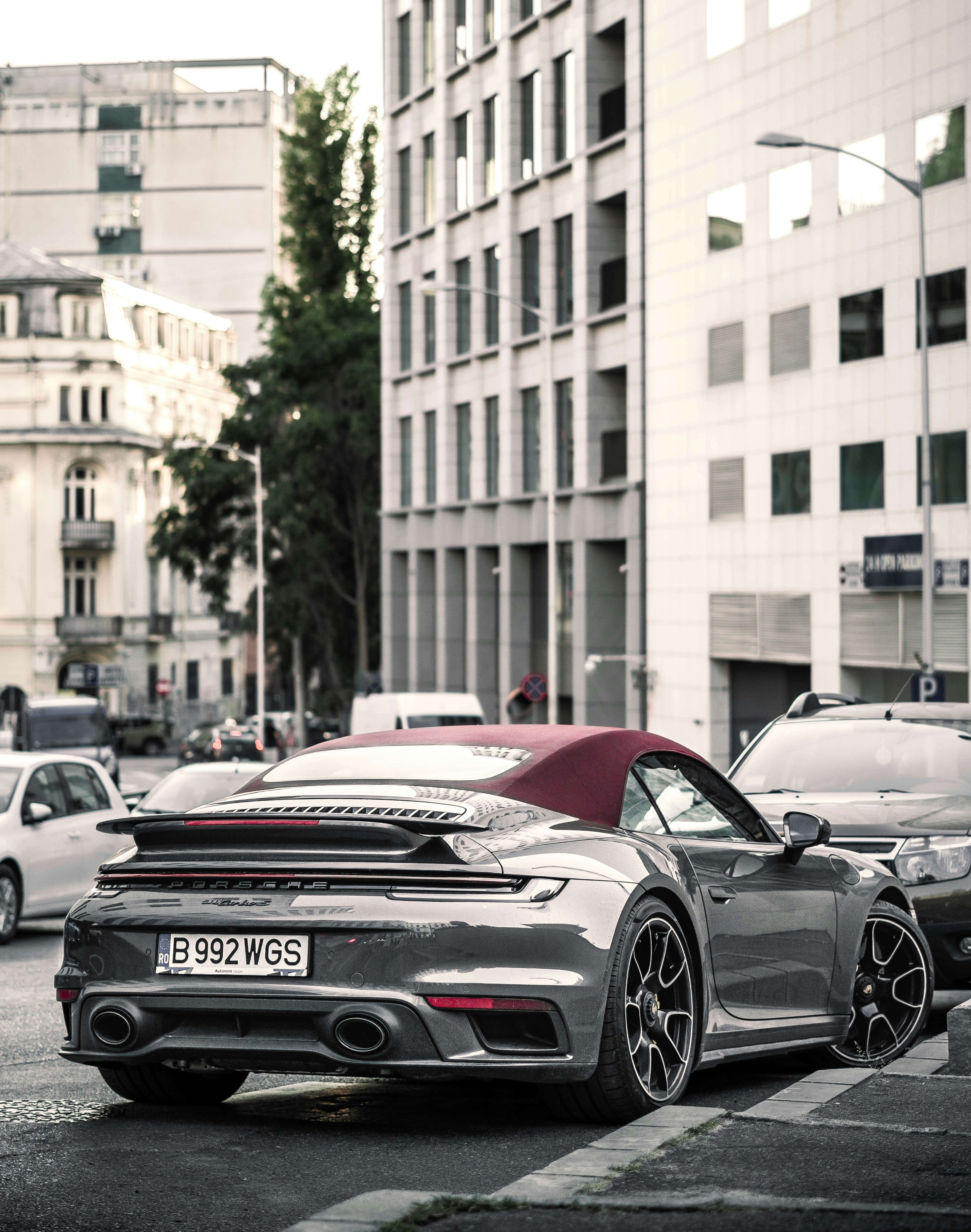 Luxury sportscar with a distinctive red convertible roof parked on a bustling city street, surrounded by urban architecture.