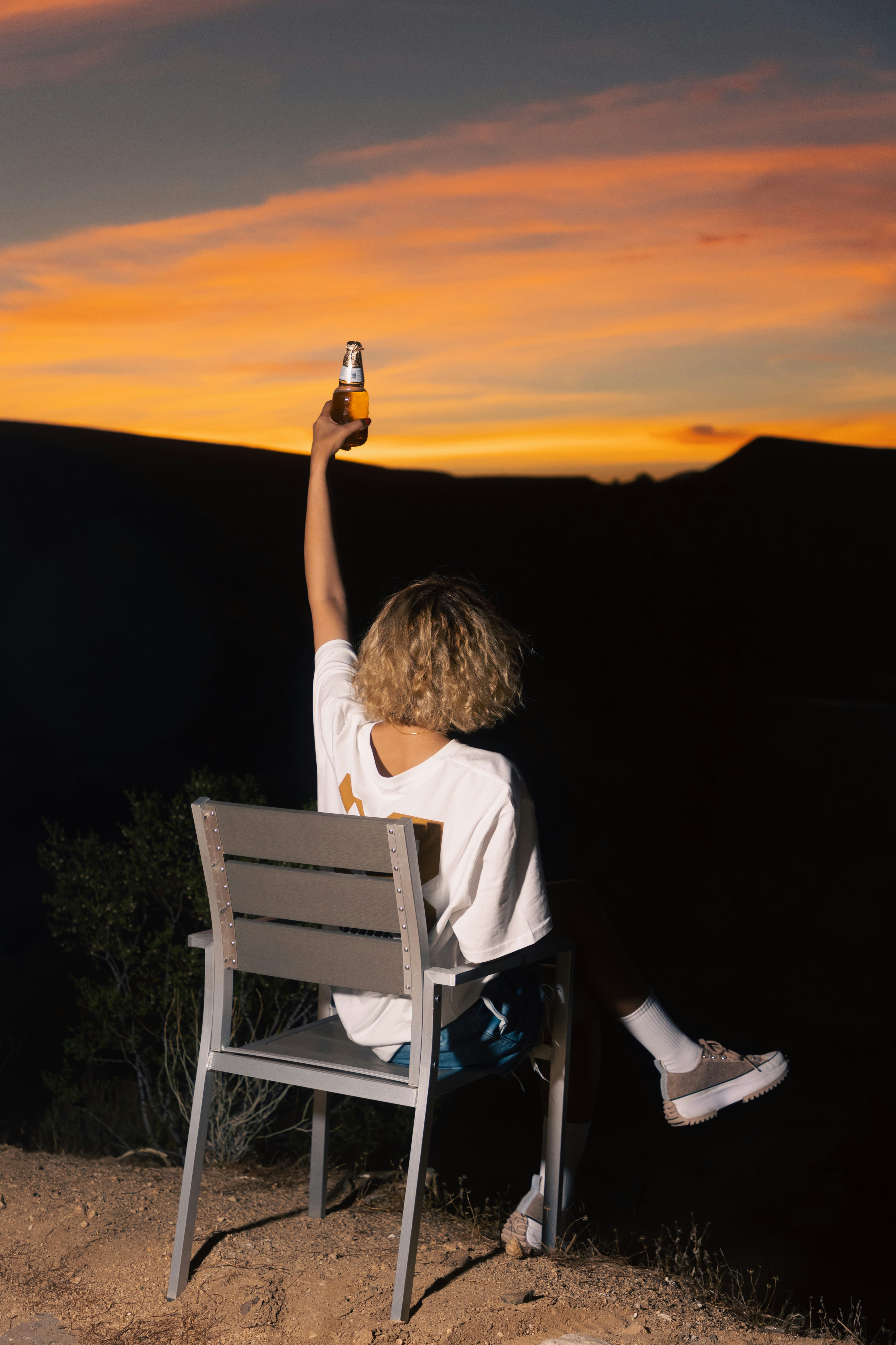 Dusk Toast from the Edge: A hillside chair, a raised beer, and a sunset blaze