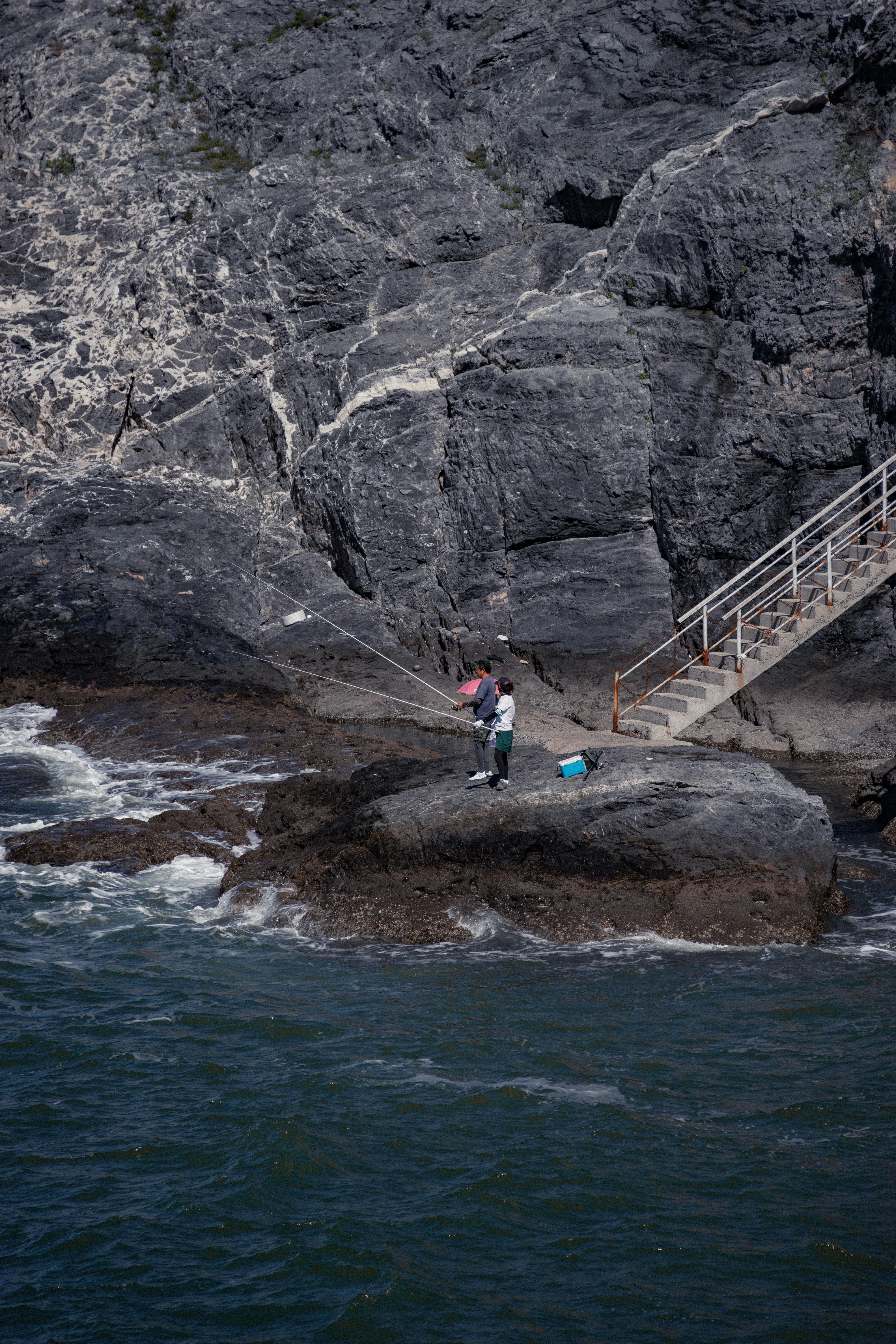 a couple of people on a rock by a body of water