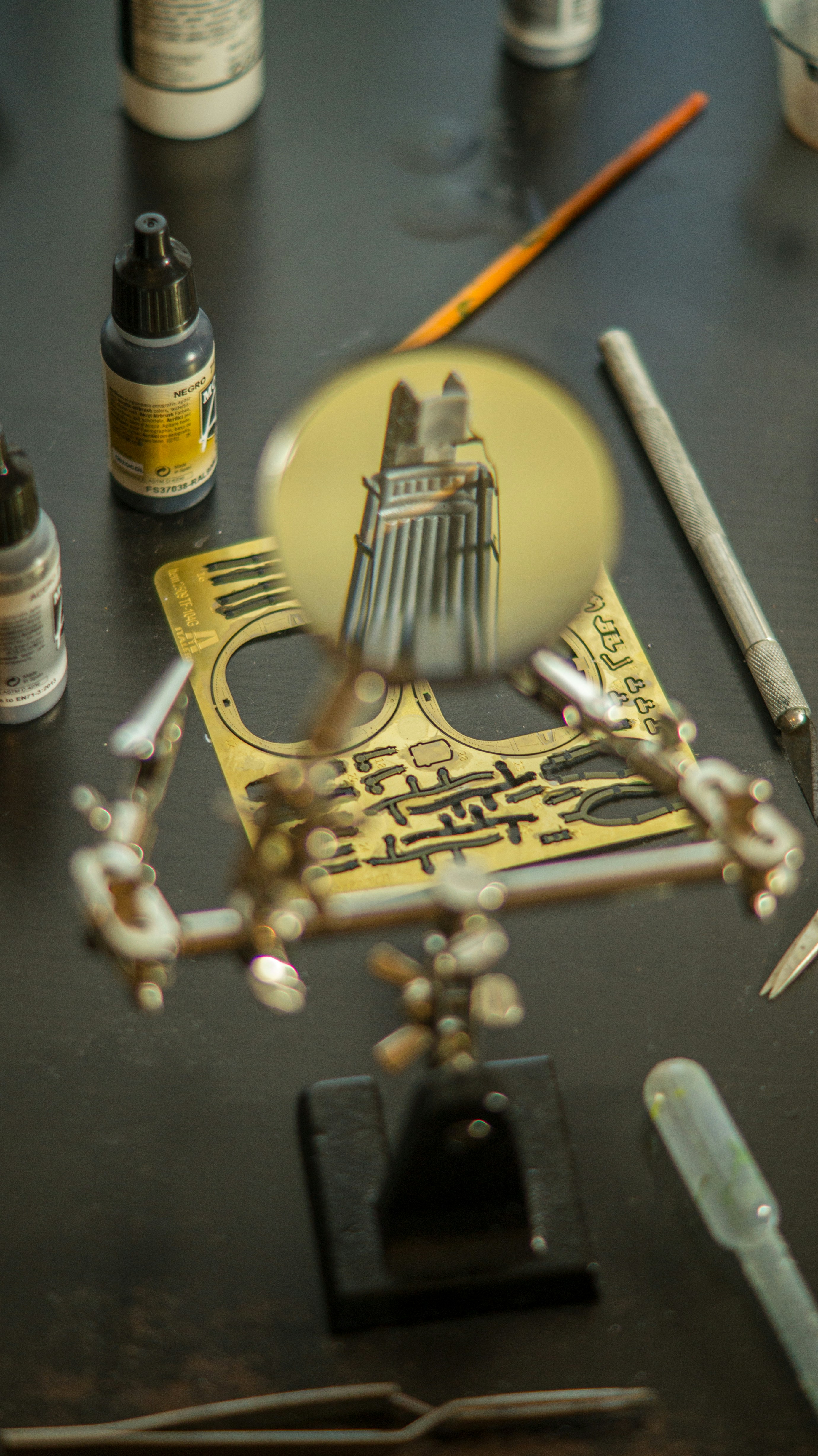Close-up of a magnifying glass reflecting intricate tools and materials on a craftsman's desk, highlighting the artistry in model assembly.