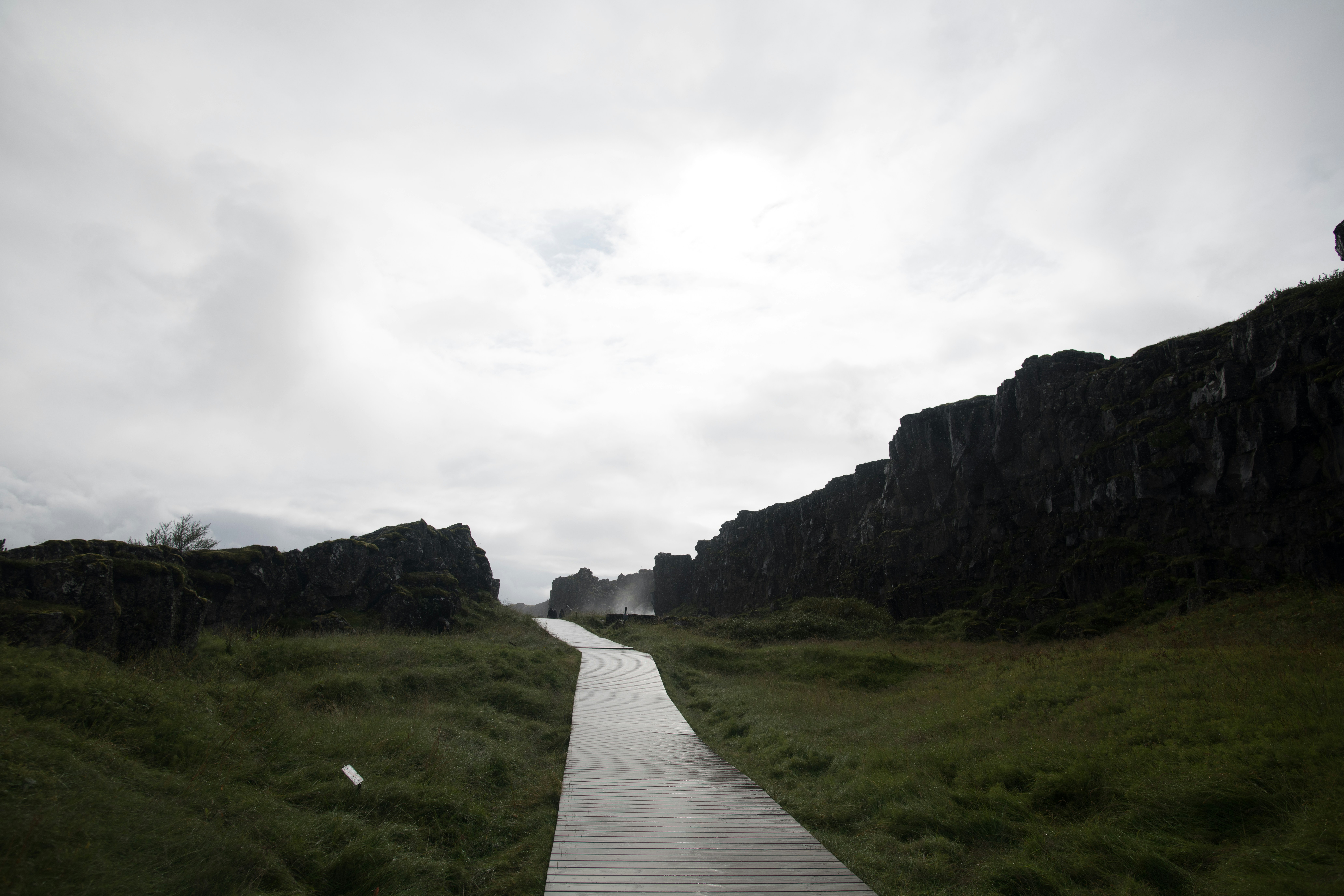 Wooden pathway leading through rugged terrain and rocky cliffs under a cloudy sky.