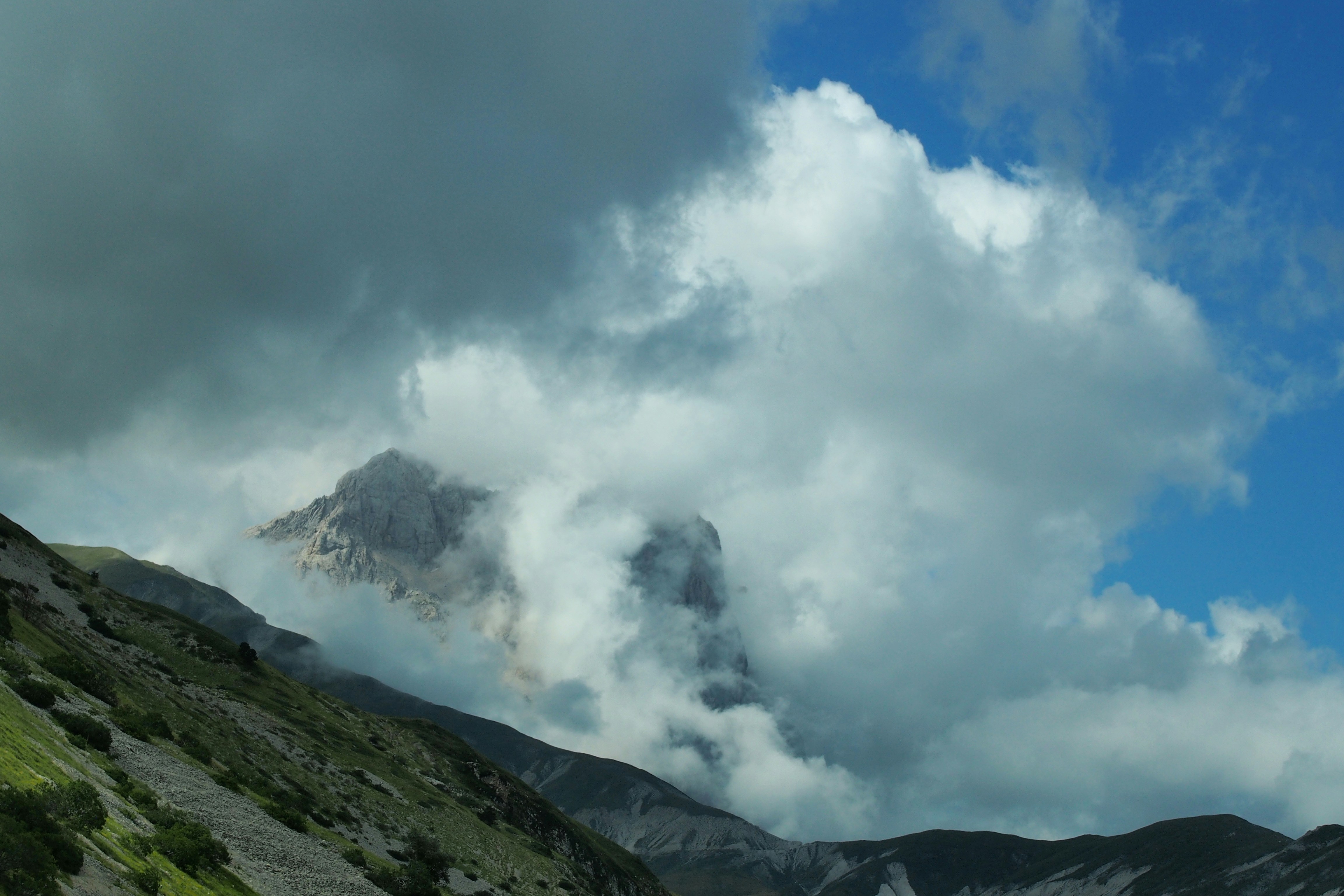 Clouds envelop the rocky summit of Gran Sasso d'Italia beneath a vibrant blue sky.