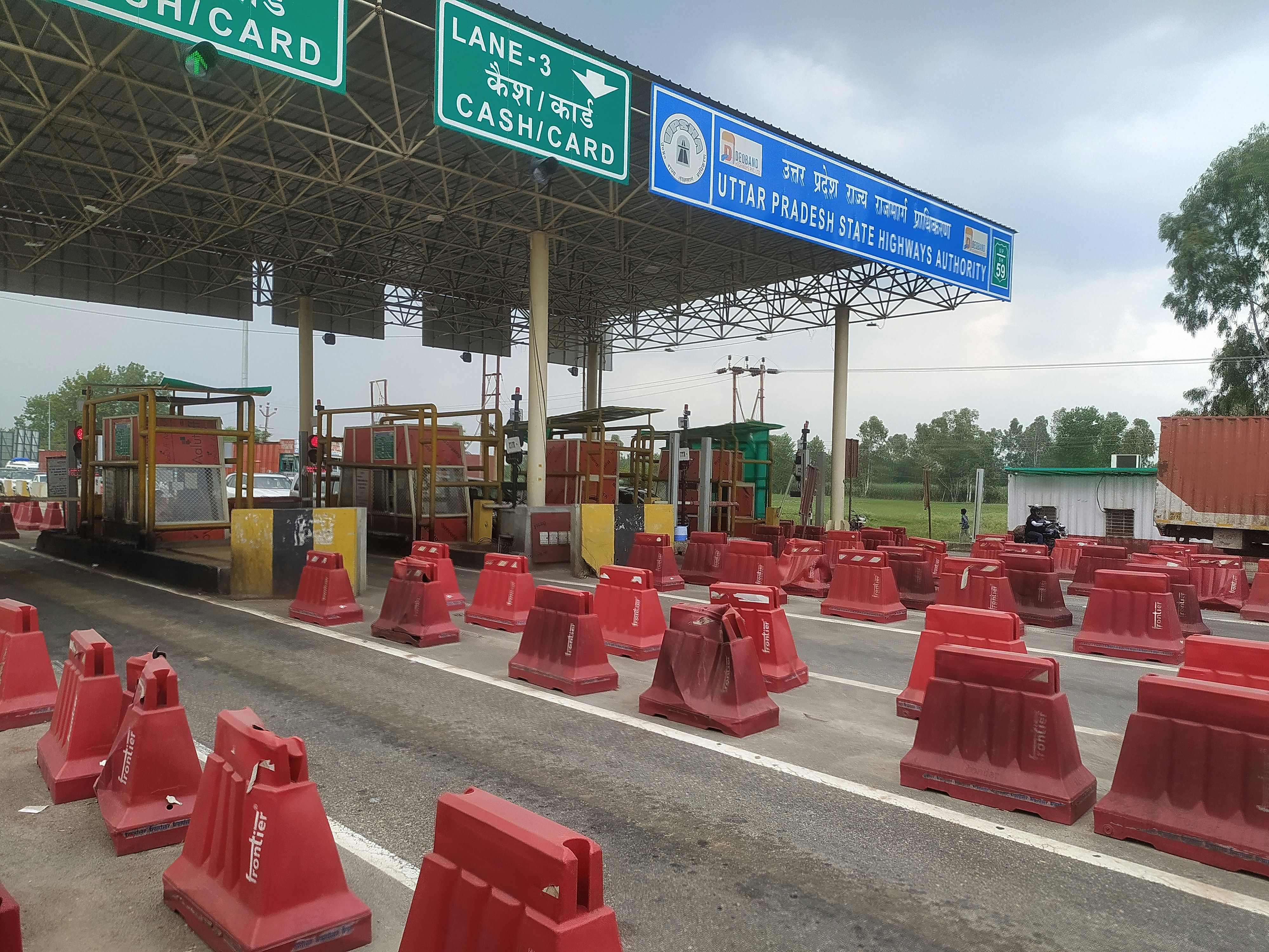Toll plaza on a highway with red barriers and directional signs under a cloudy sky.