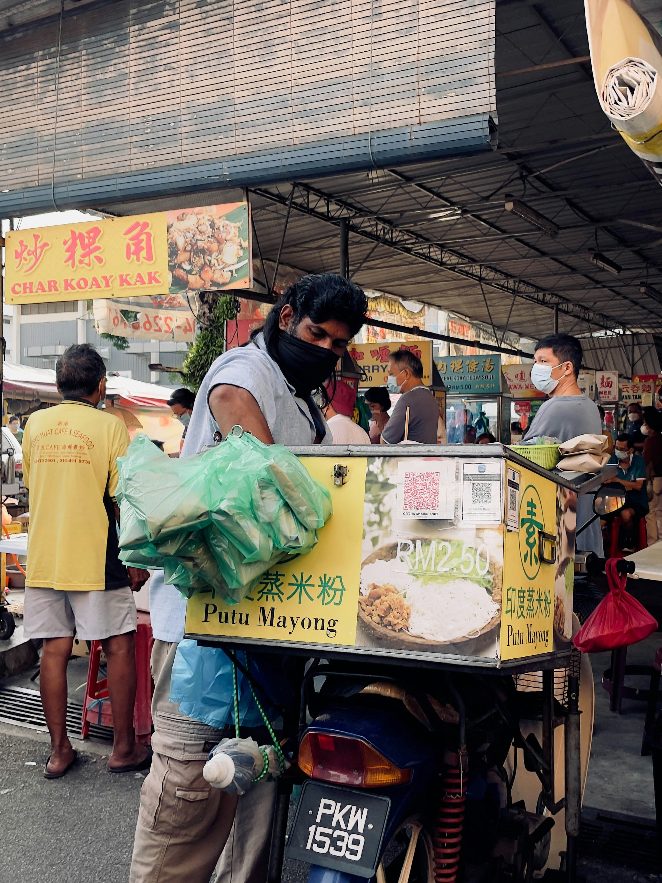 Vendor preparing traditional Putu Mayong amidst a bustling street market filled with colorful stalls and eager customers.