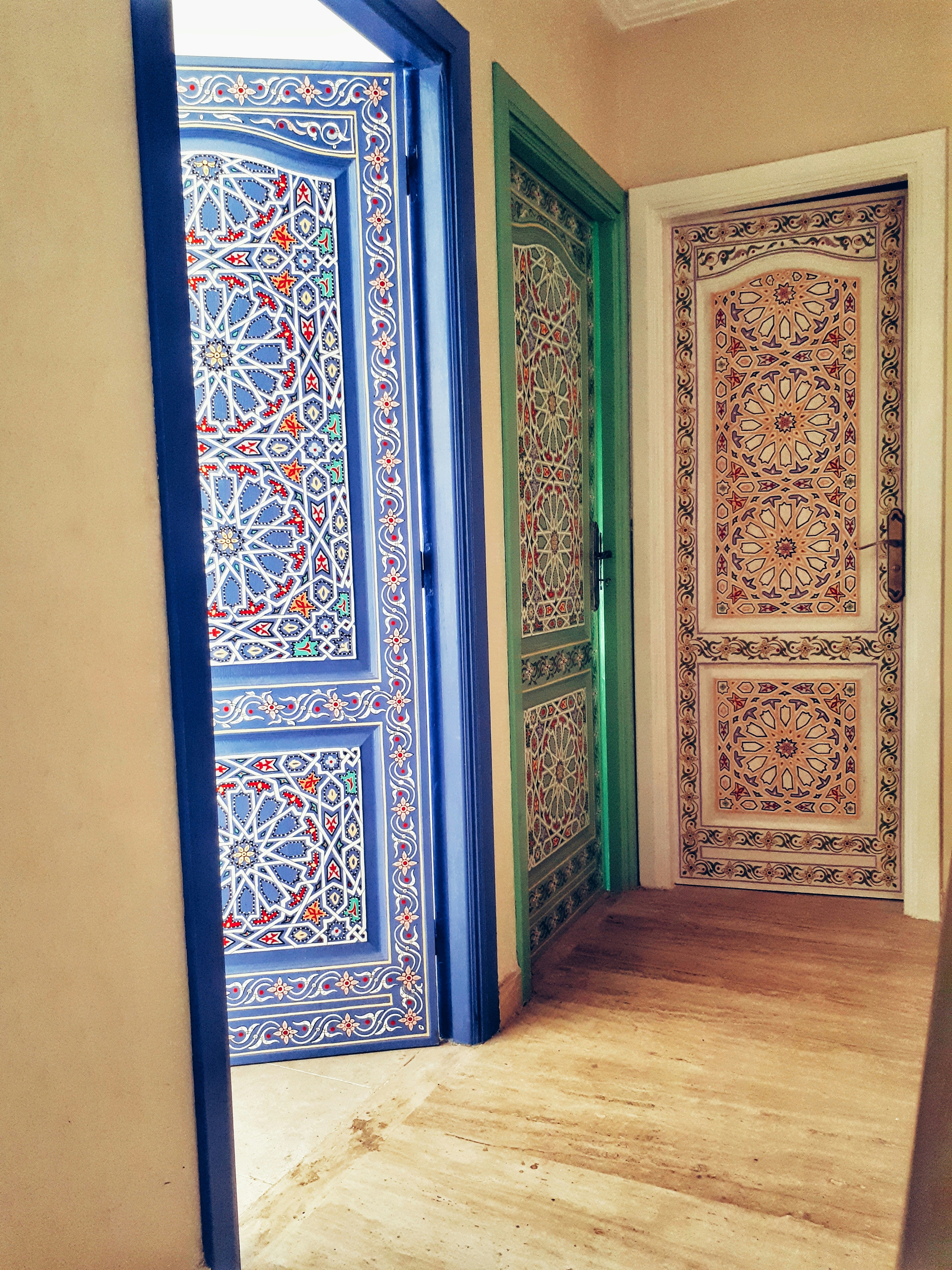 Three intricately designed doors in a corridor, showcasing vibrant patterns and colors. The interplay of light and shadow enhances the architectural beauty.