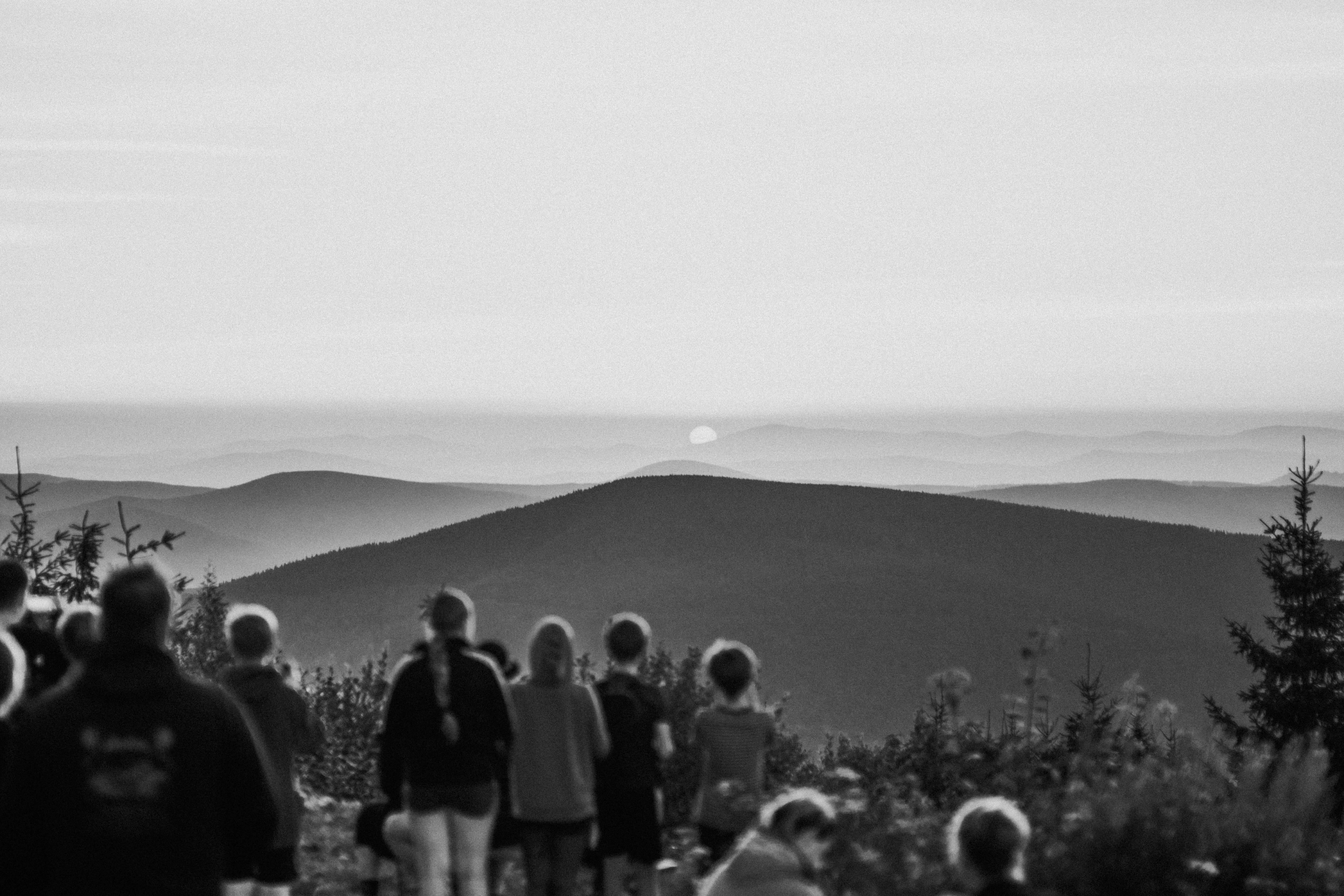 Group of people watching the sunrise over distant rolling hills and valleys.