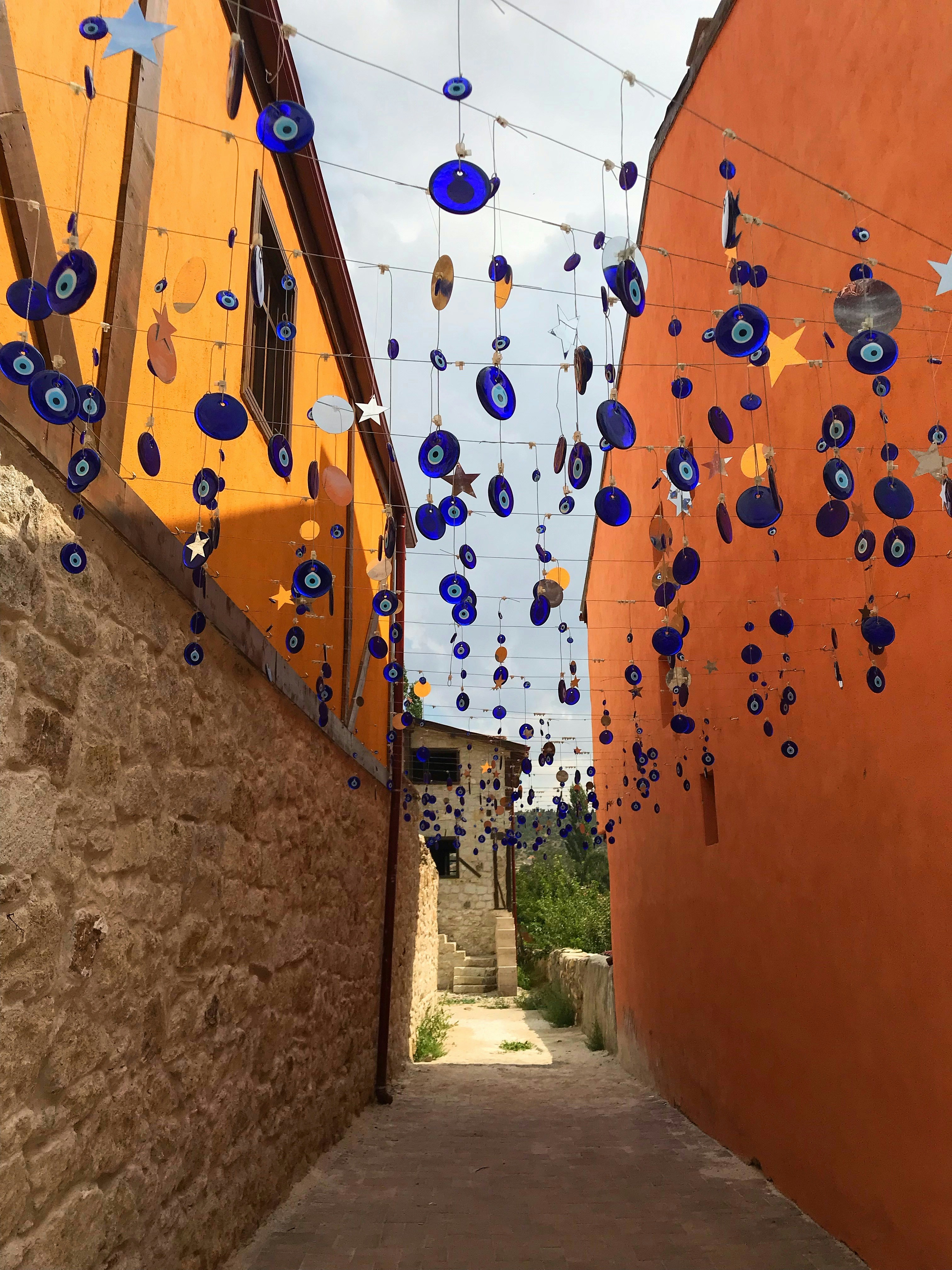Narrow alley adorned with blue glass ornaments and stars strung between vibrant orange walls.