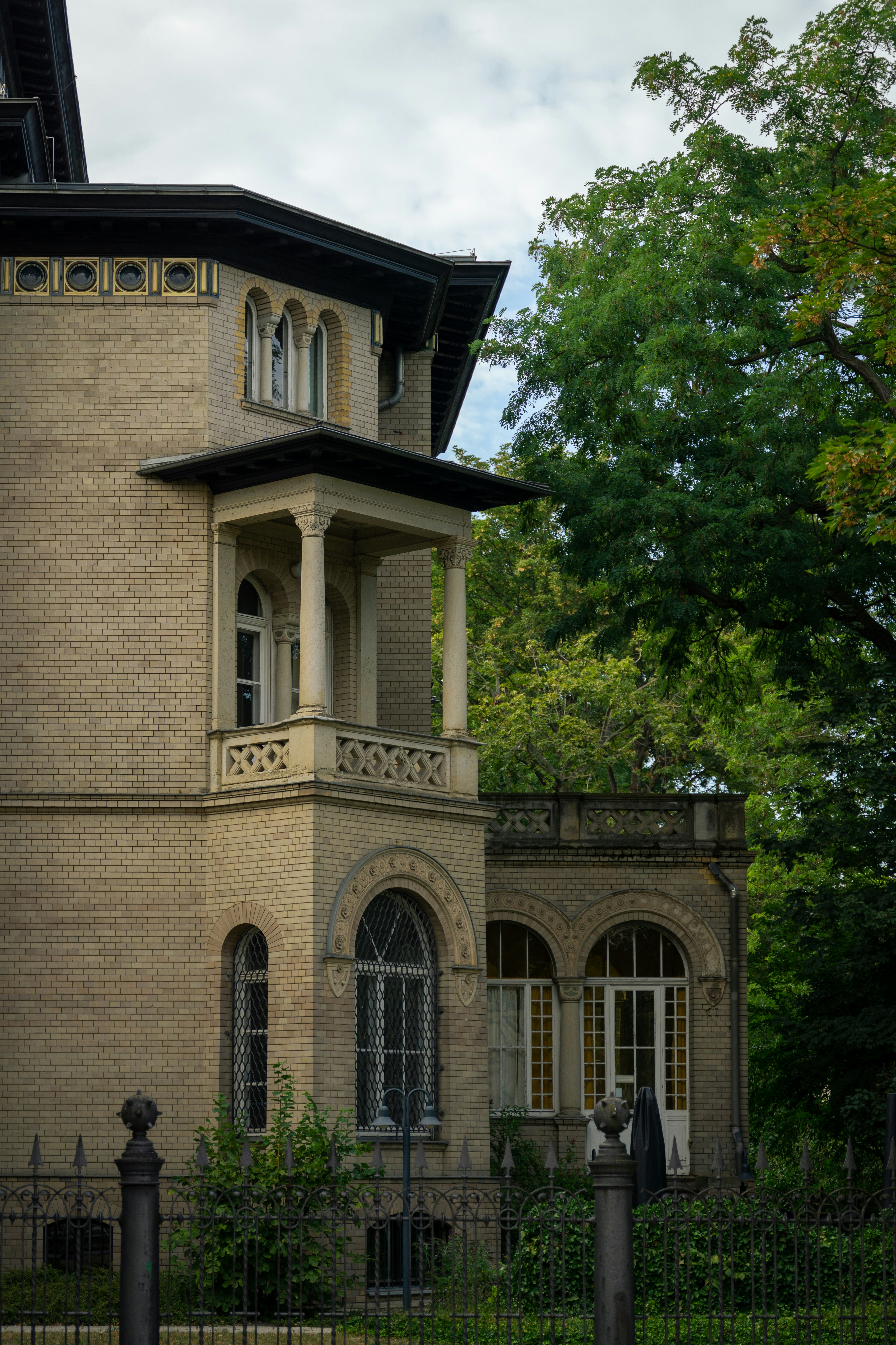 Amber Brick Villa: Arched Windows, Columned Balcony, and Iron Fence Under a Green Canopy