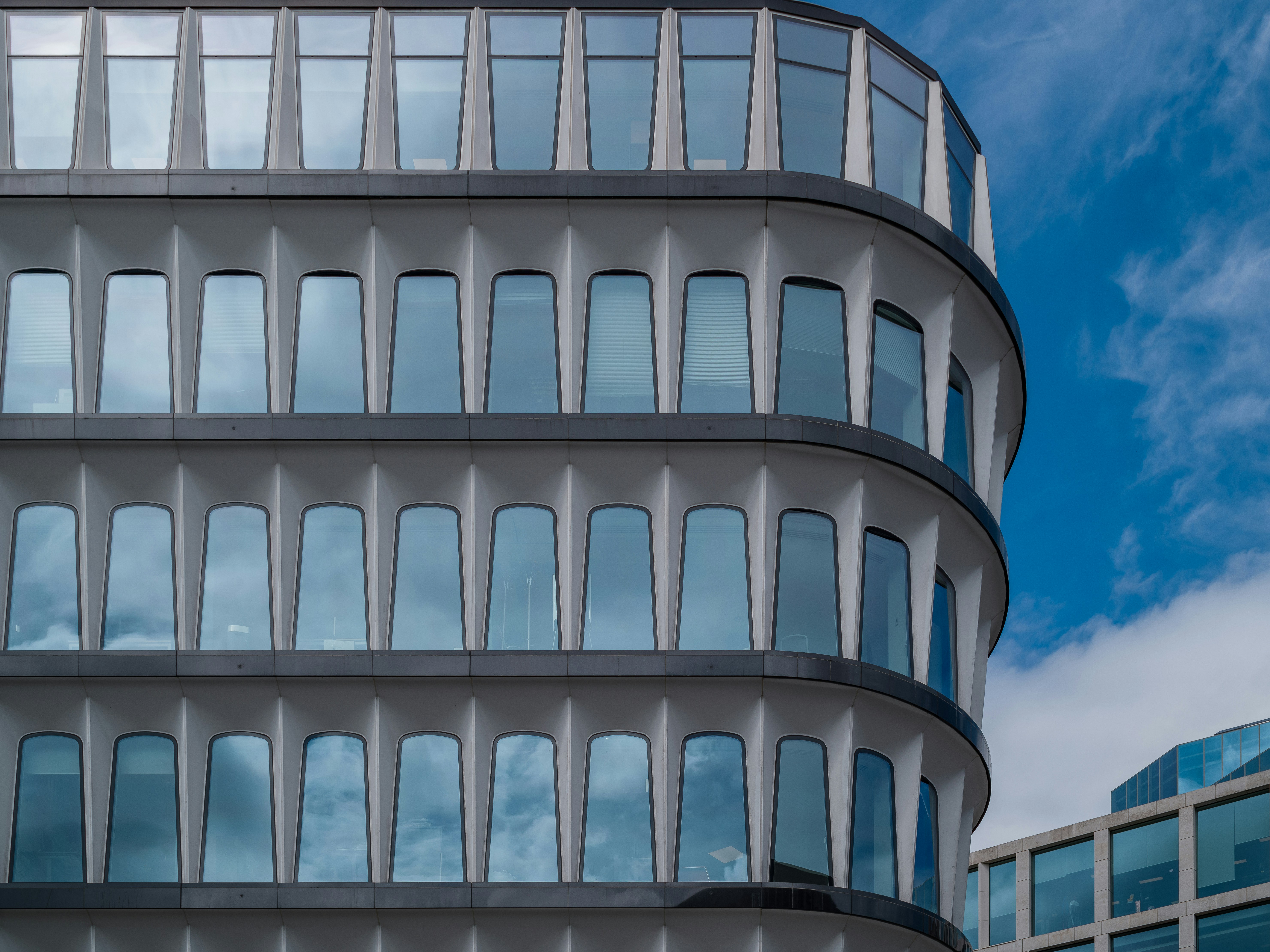 Curved glass facade of a modern building reflecting the sky and clouds.