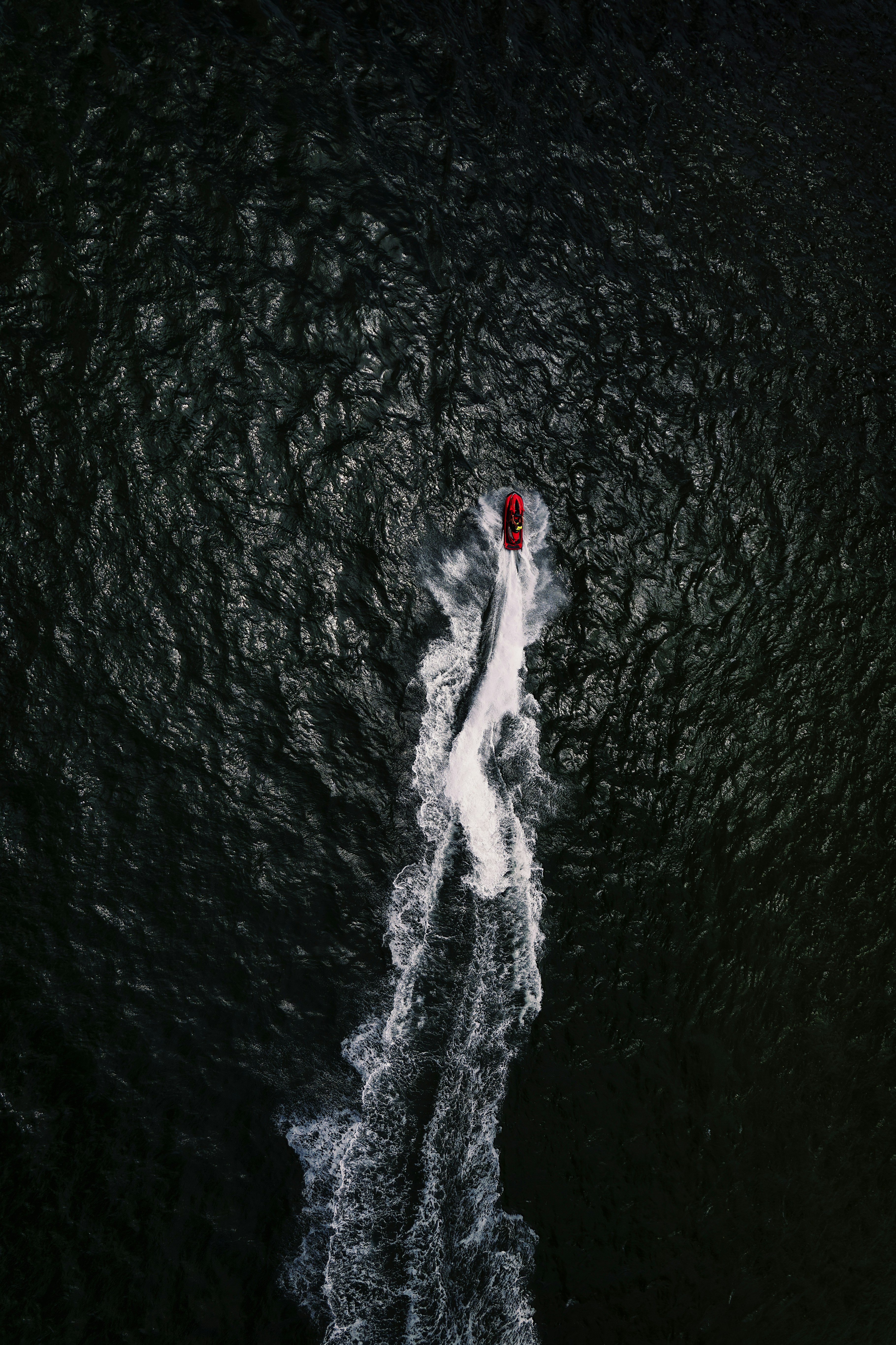 Red Speedboat Slices a White Wake Through a Dark, Textured Sea