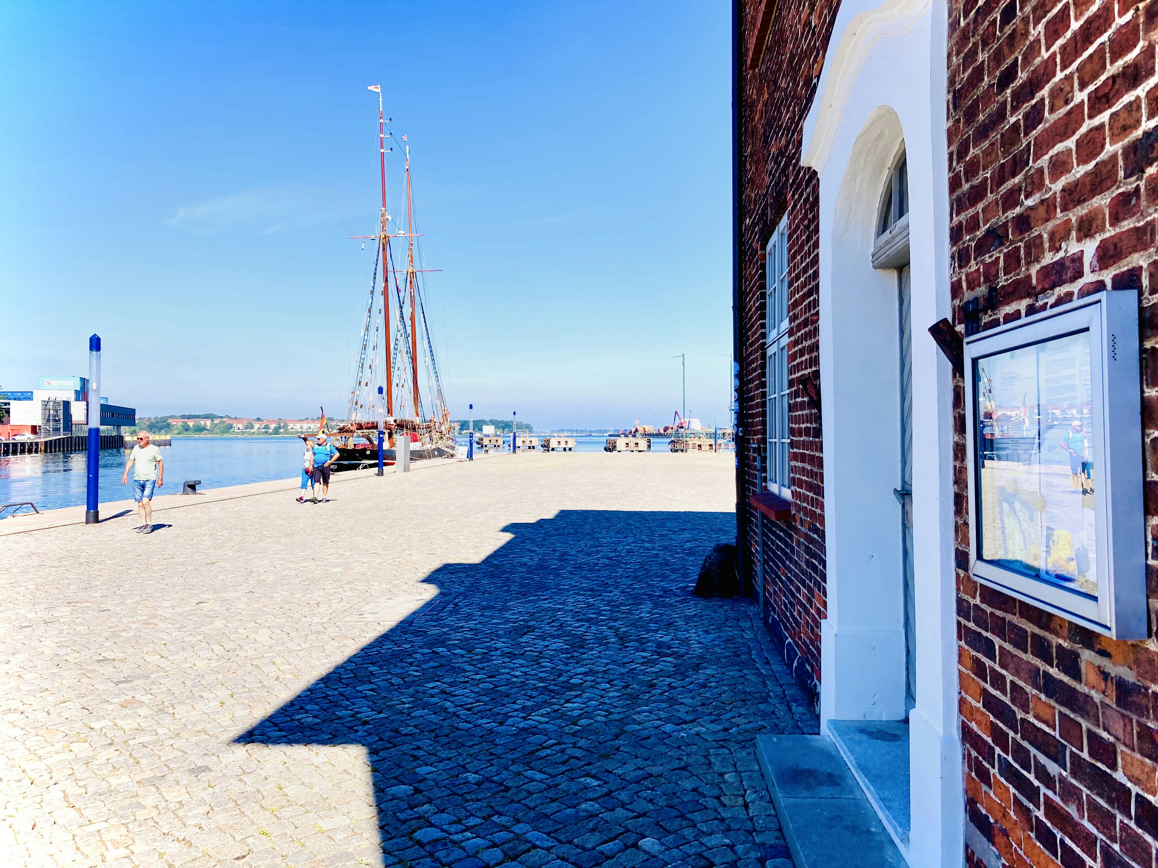 Harbor Geometry: Sail Masts Against a Sunlit Cobblestone Pier