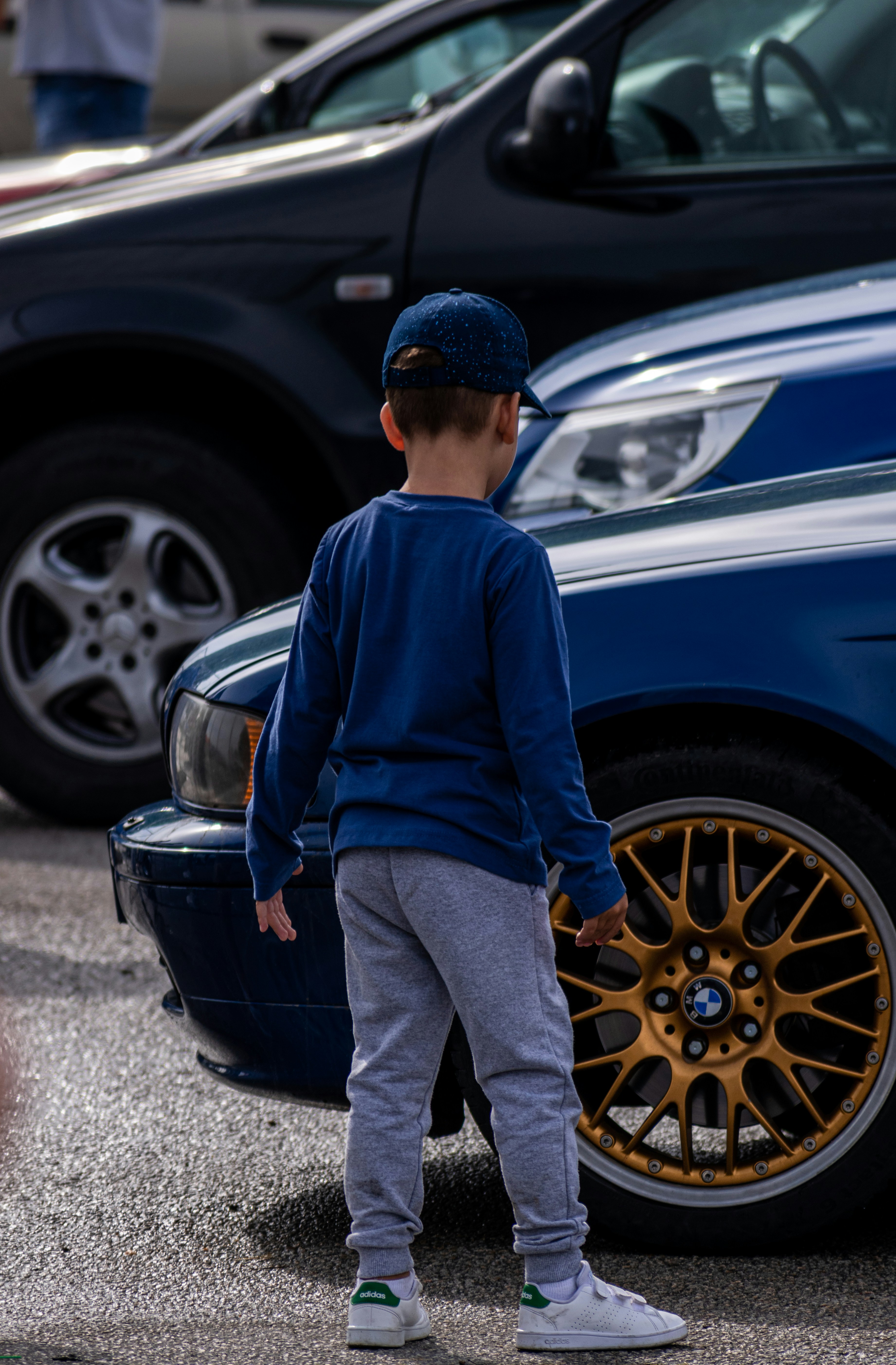 Curious Blue-Hooded Boy Pausing Before a Gold-Spoked Car Wheel
