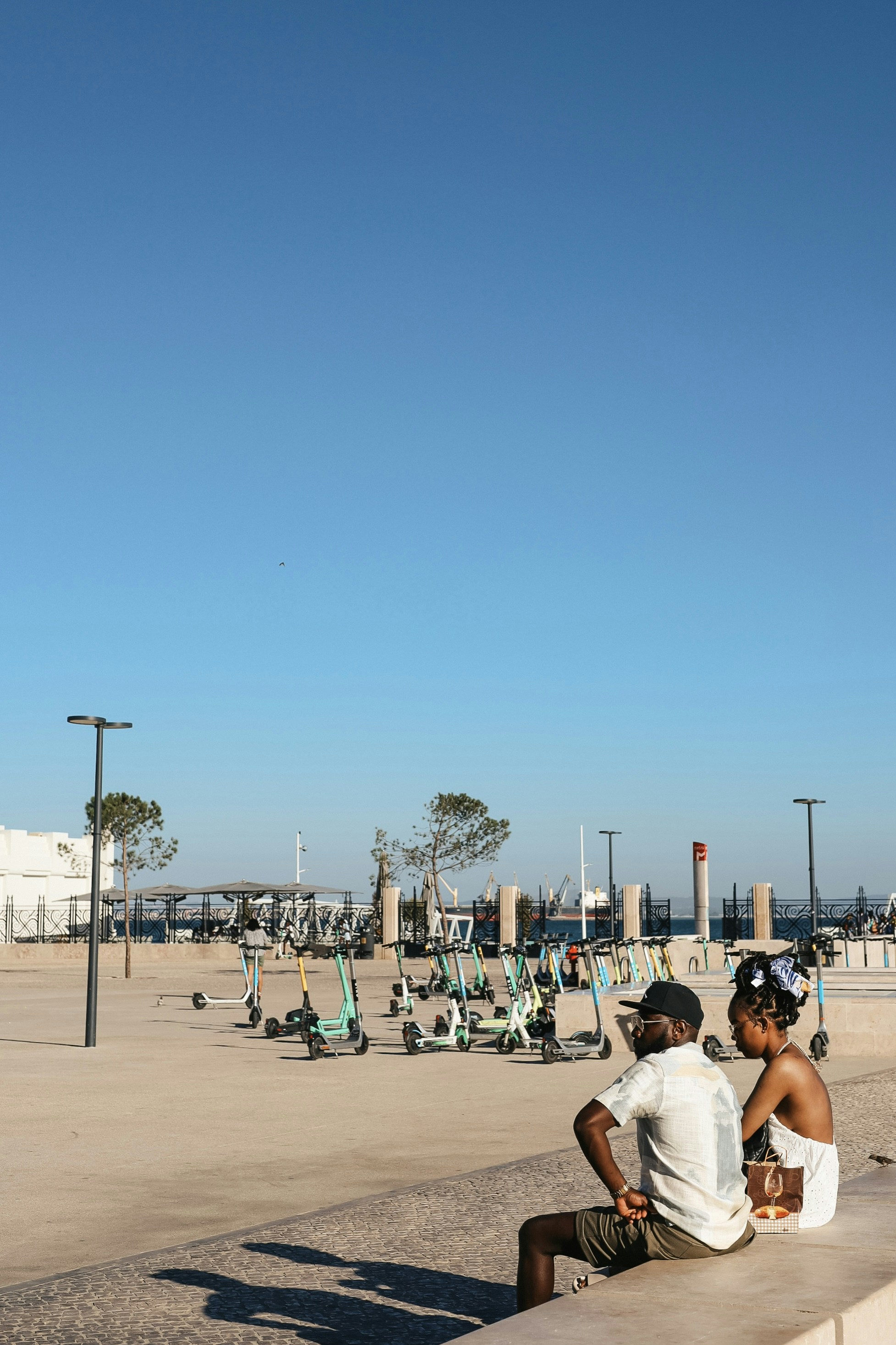 Riverside Pause: A Couple on a Sunlit Promenade with Lime Scooters in the Background