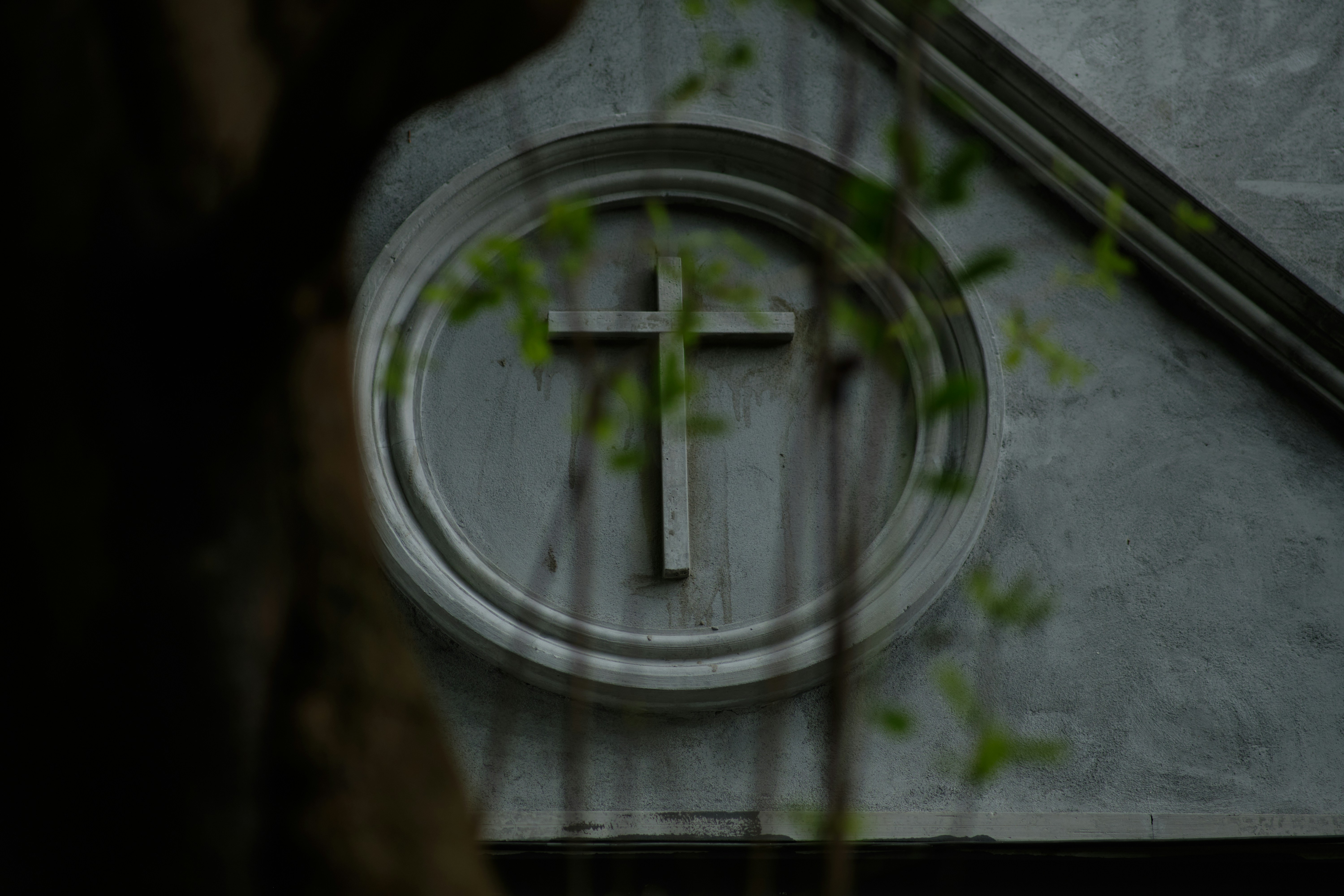 Metal cross on a circular plaque surrounded by soft shadows and leaves.