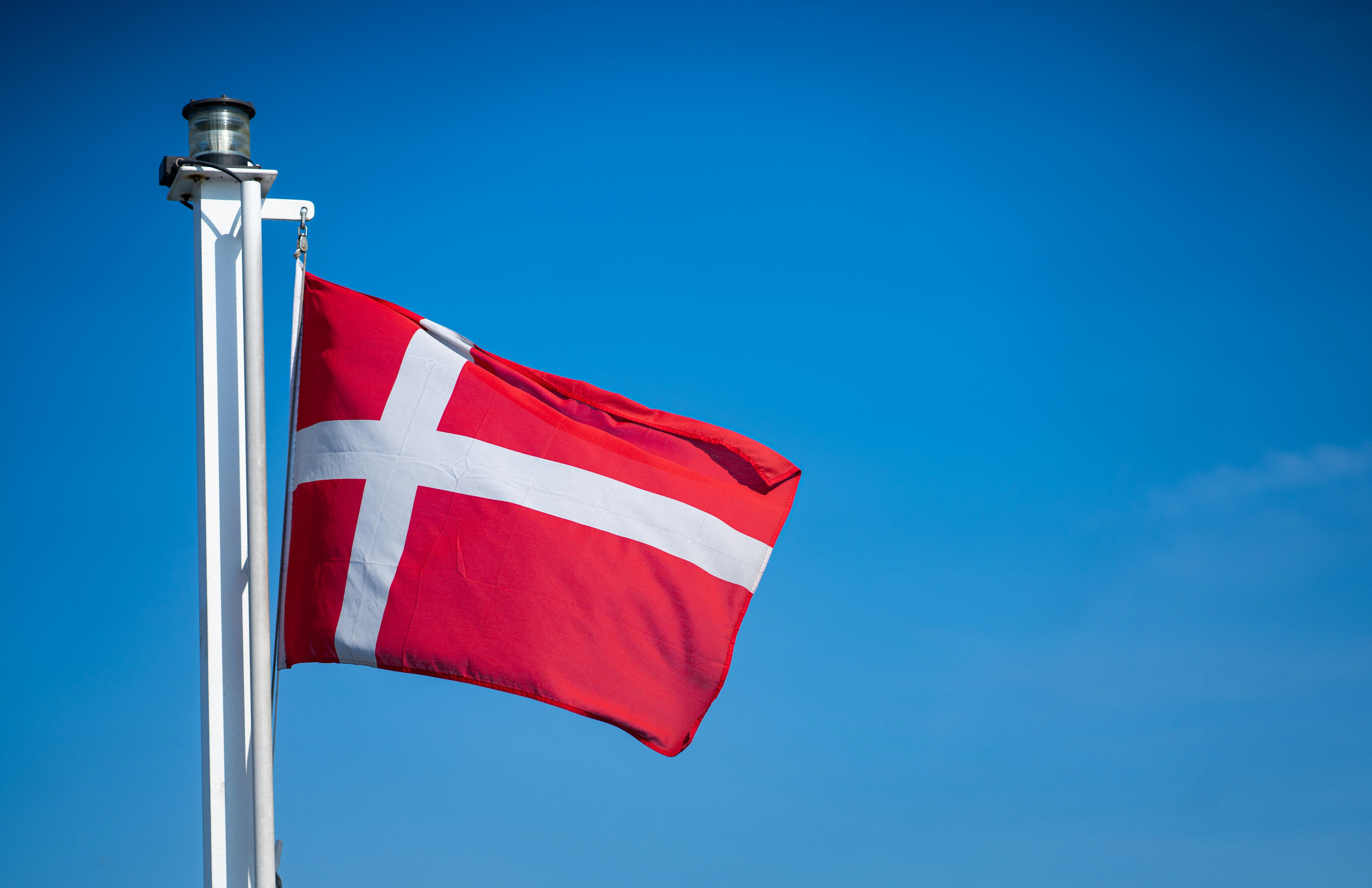Danish flag fluttering against a clear blue sky, symbolizing national pride and identity.