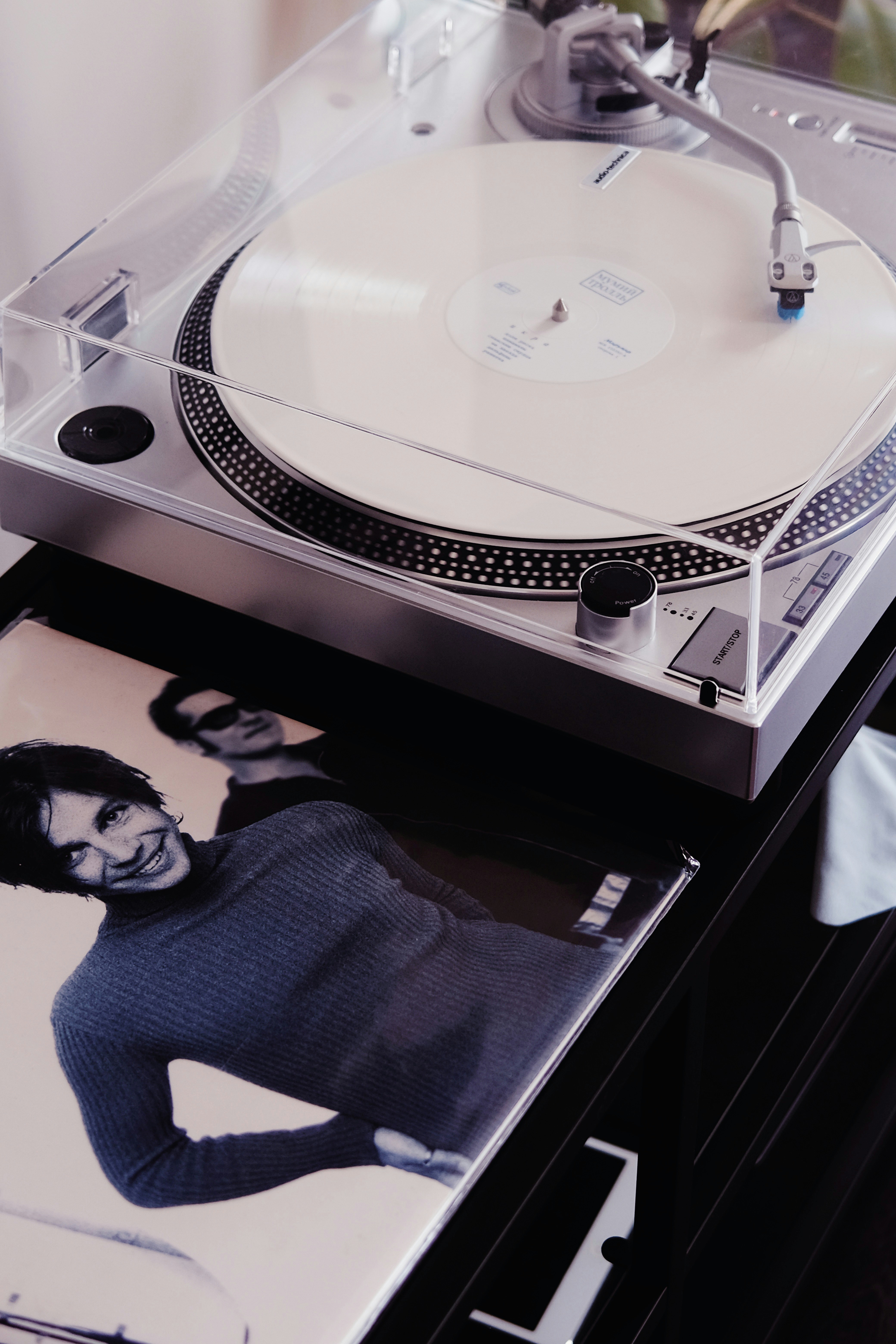 A vintage turntable with a vinyl record playing, accompanied by an album cover featuring a smiling musician. The scene evokes nostalgia and a love for music.