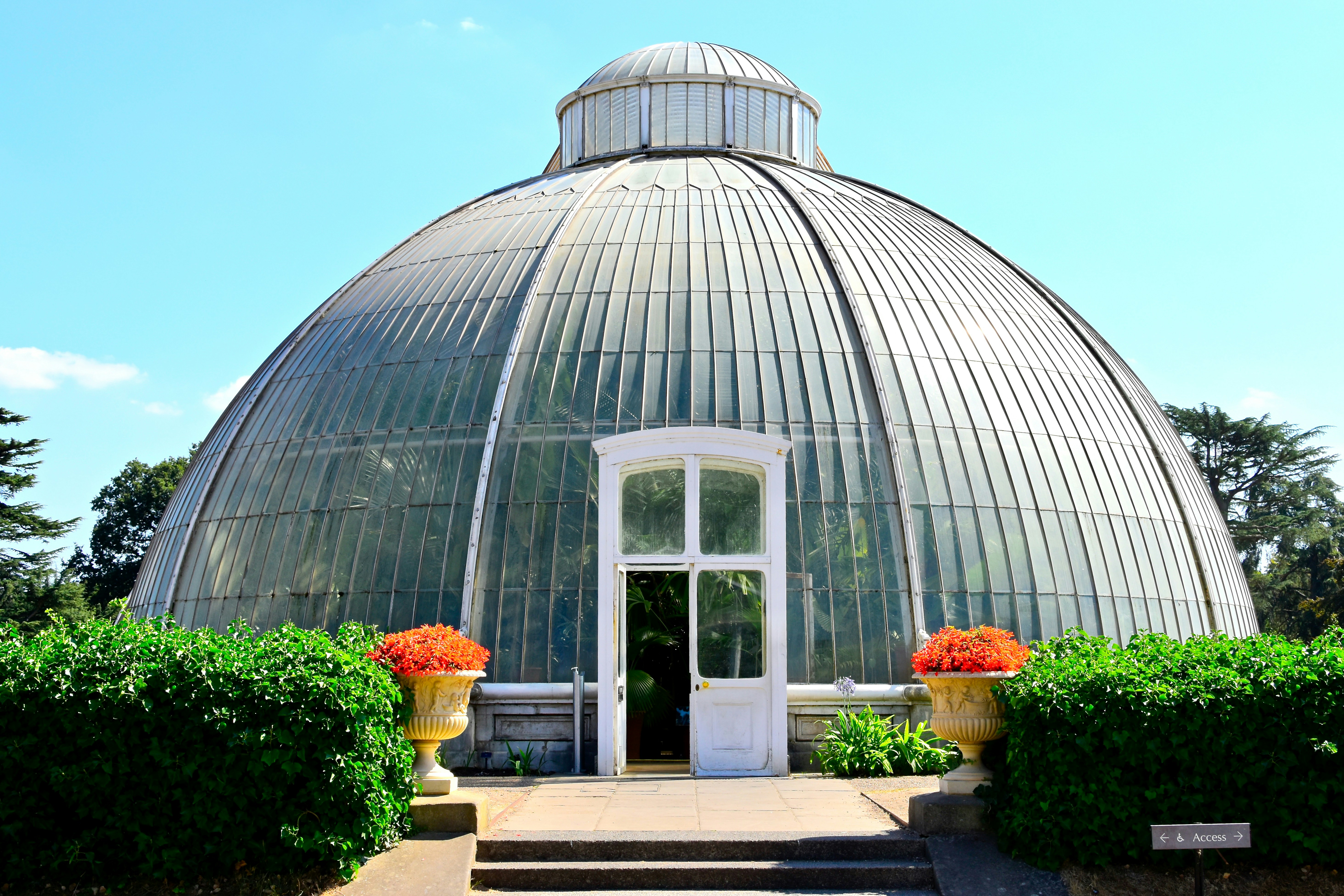 A large, domed greenhouse with glass panels and vibrant flower pots at its entrance, showcasing an elegant blend of nature and architecture.