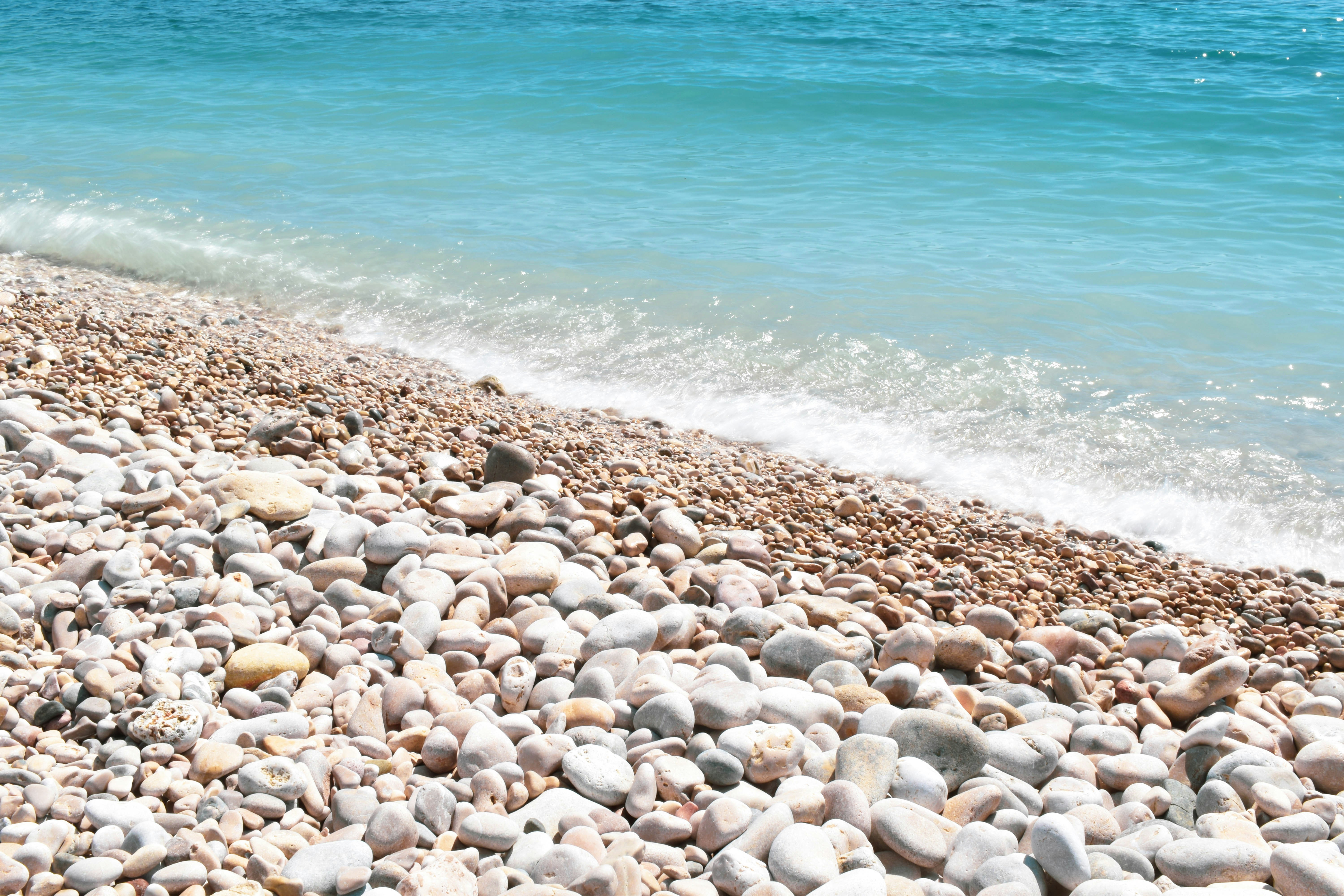 Smooth pebbles line a serene beach, kissed by gentle waves and glistening under the sun. The tranquil meeting of land and sea creates a peaceful atmosphere.