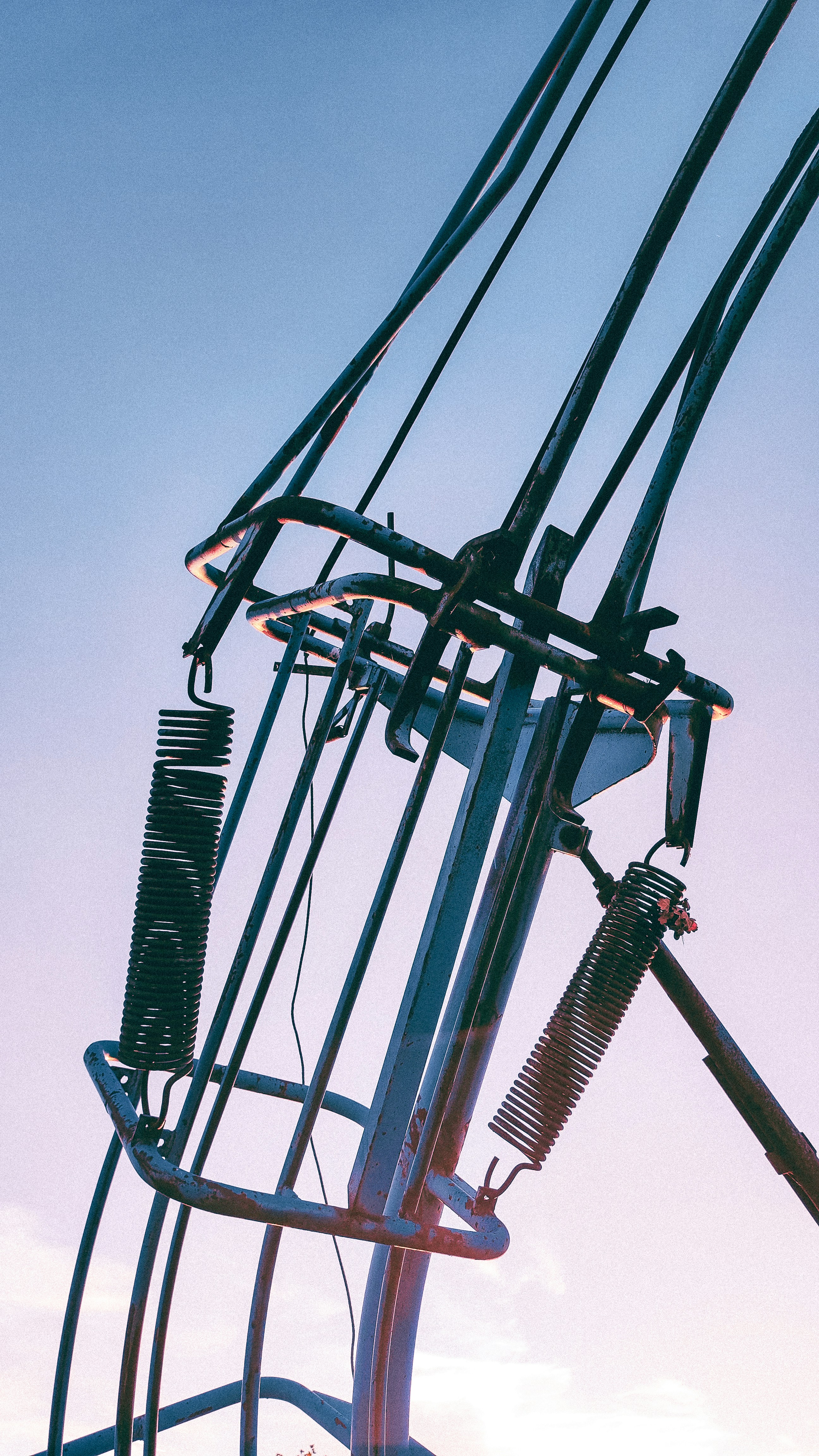 A photograph of transmission insulators and metal framework stretched across a pastel sky. Tilted composition emphasizes industrial geometry.