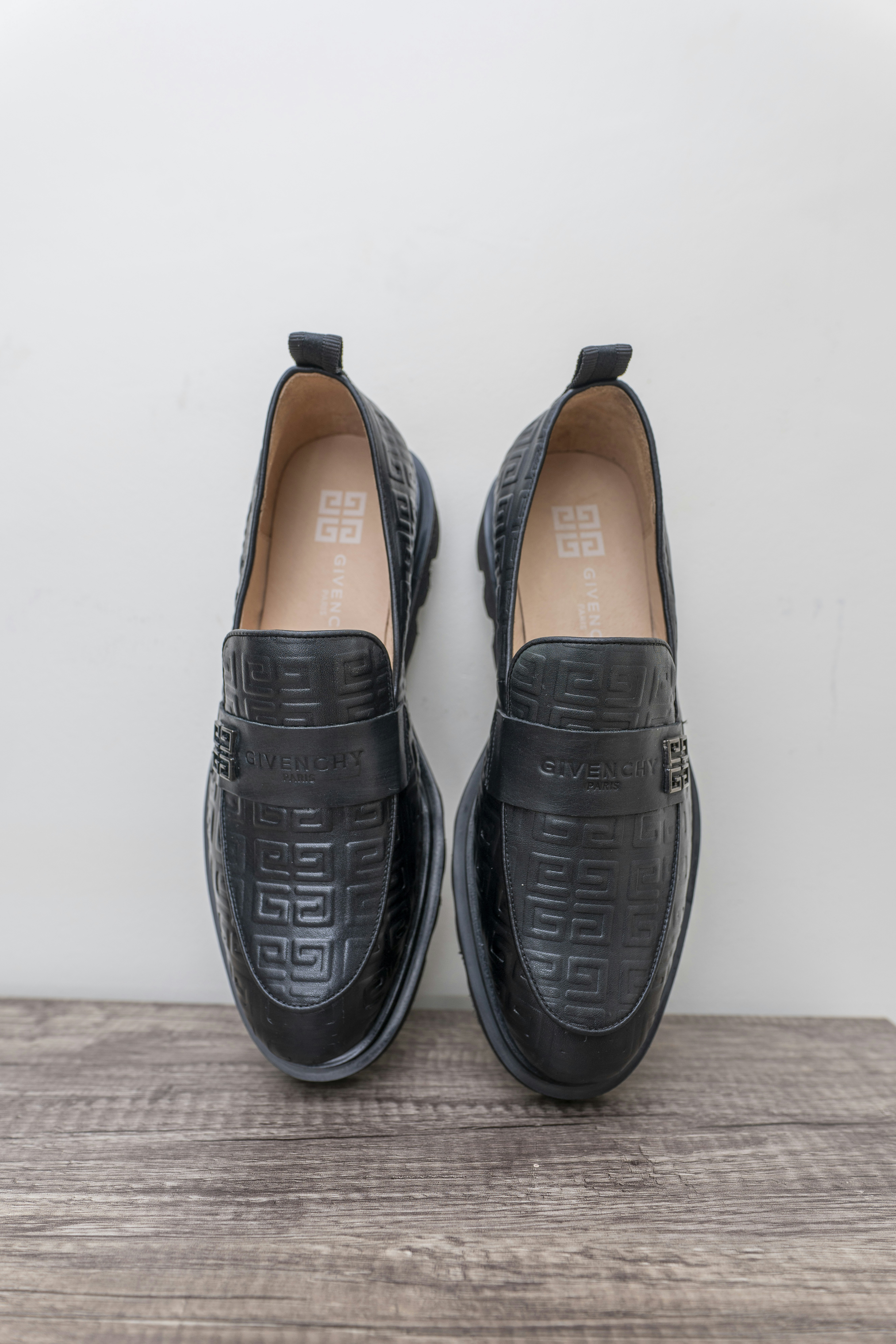 Black Givenchy loafers displayed on a wooden surface, highlighting their intricate design and luxury branding.