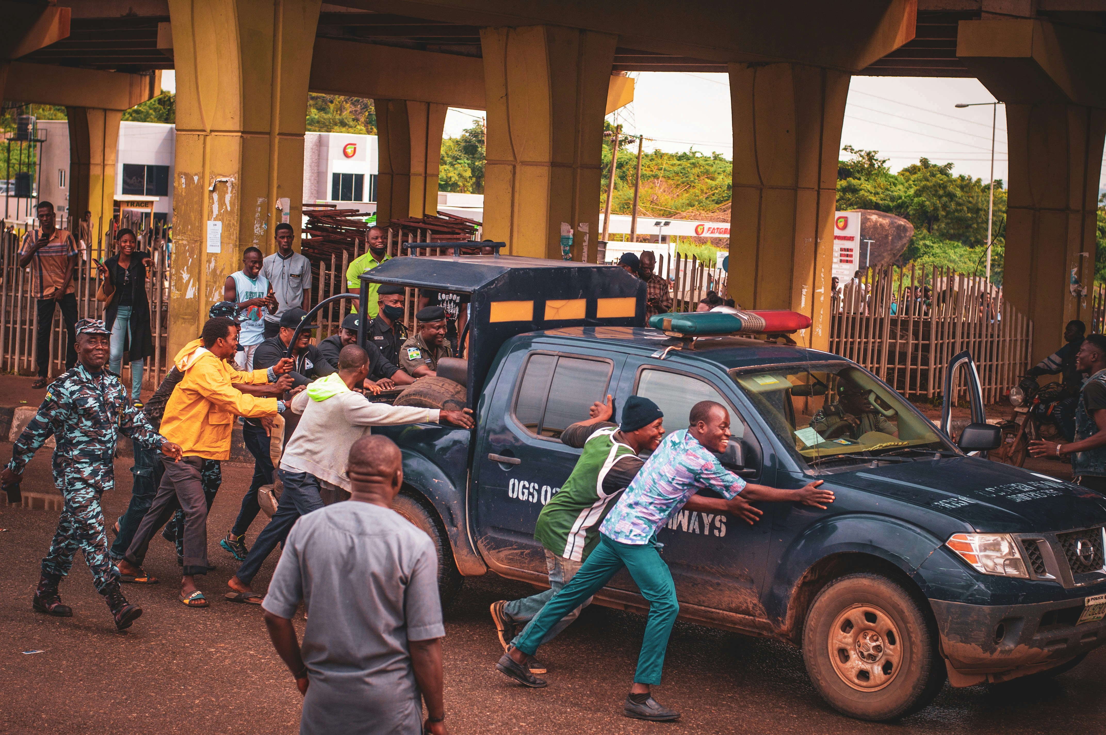Group of people pushing a vehicle under a concrete overpass.