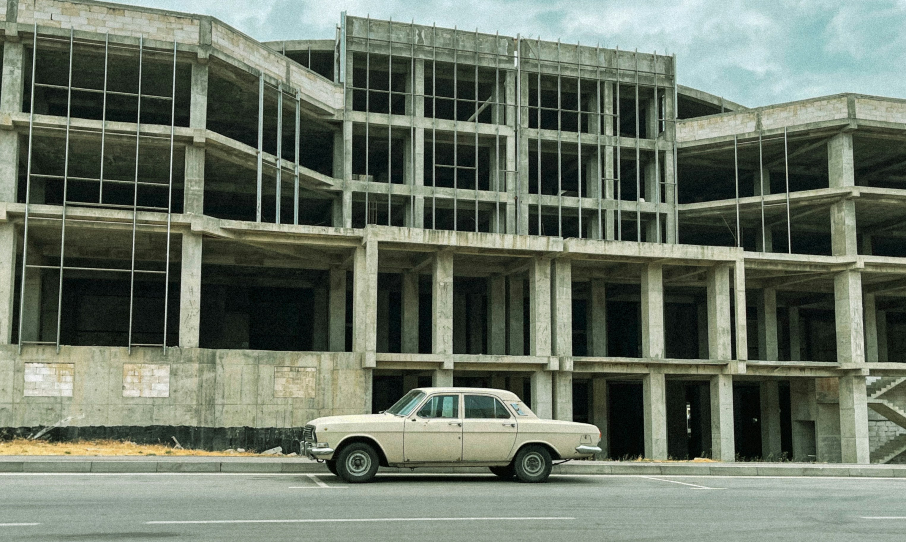A lone vintage sedan rests before a skeletal concrete shell