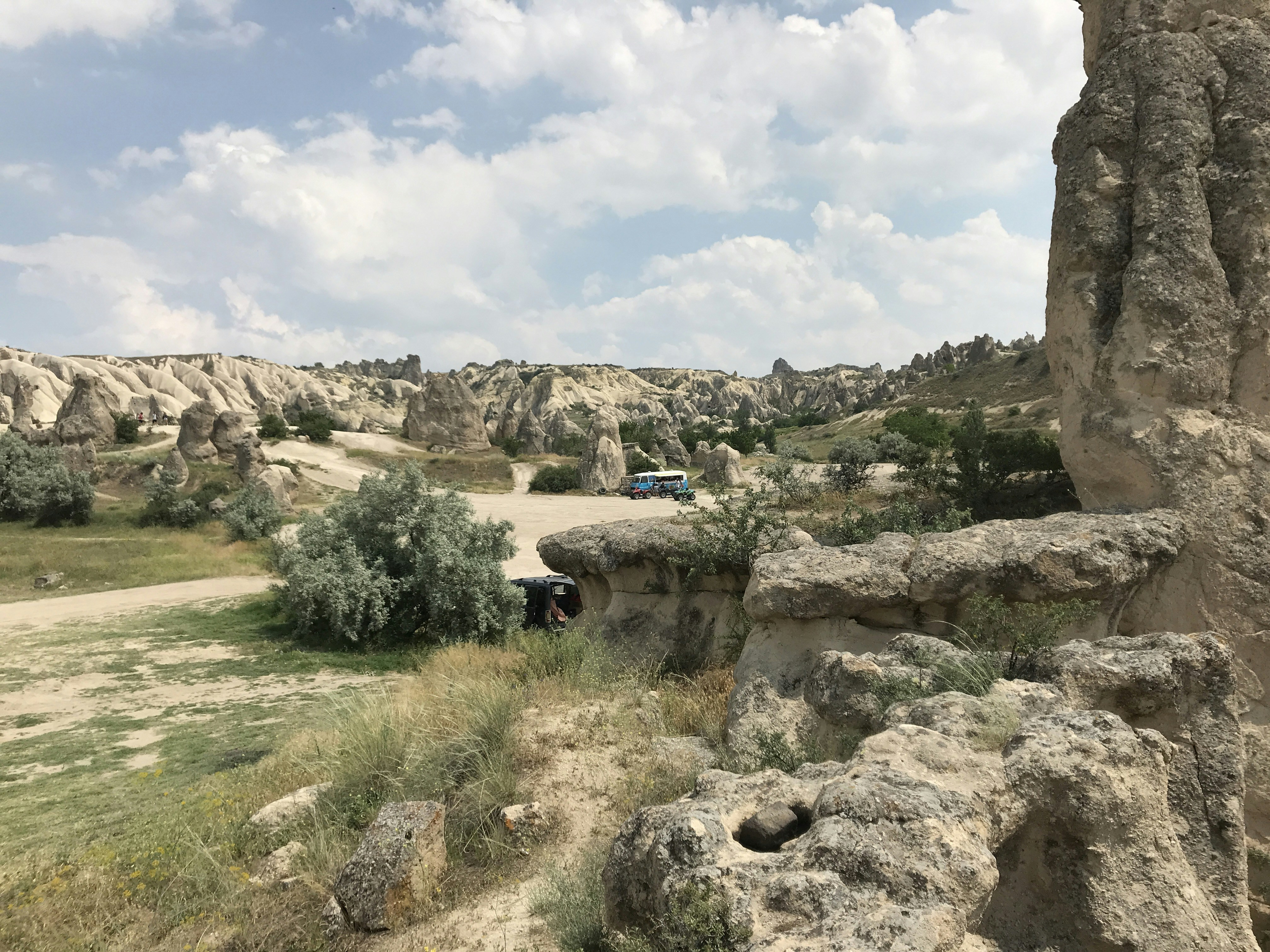 Unique rock formations rise dramatically against a cloudy sky in a serene landscape, with a hint of human presence in the distance.