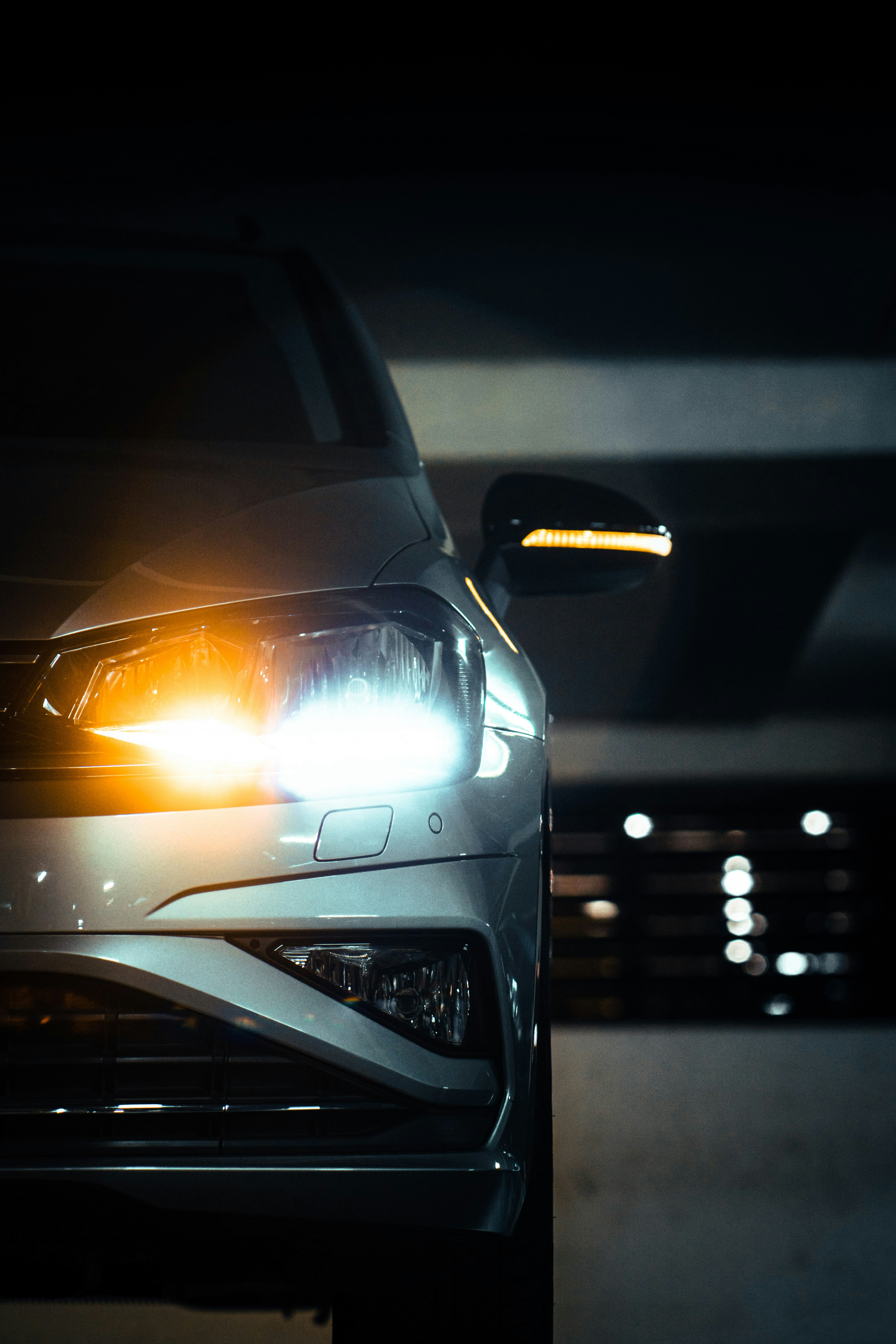 Front shot of a silver VW Sportsvan bumper with its headlights and indicator on. | a car with its headlights on