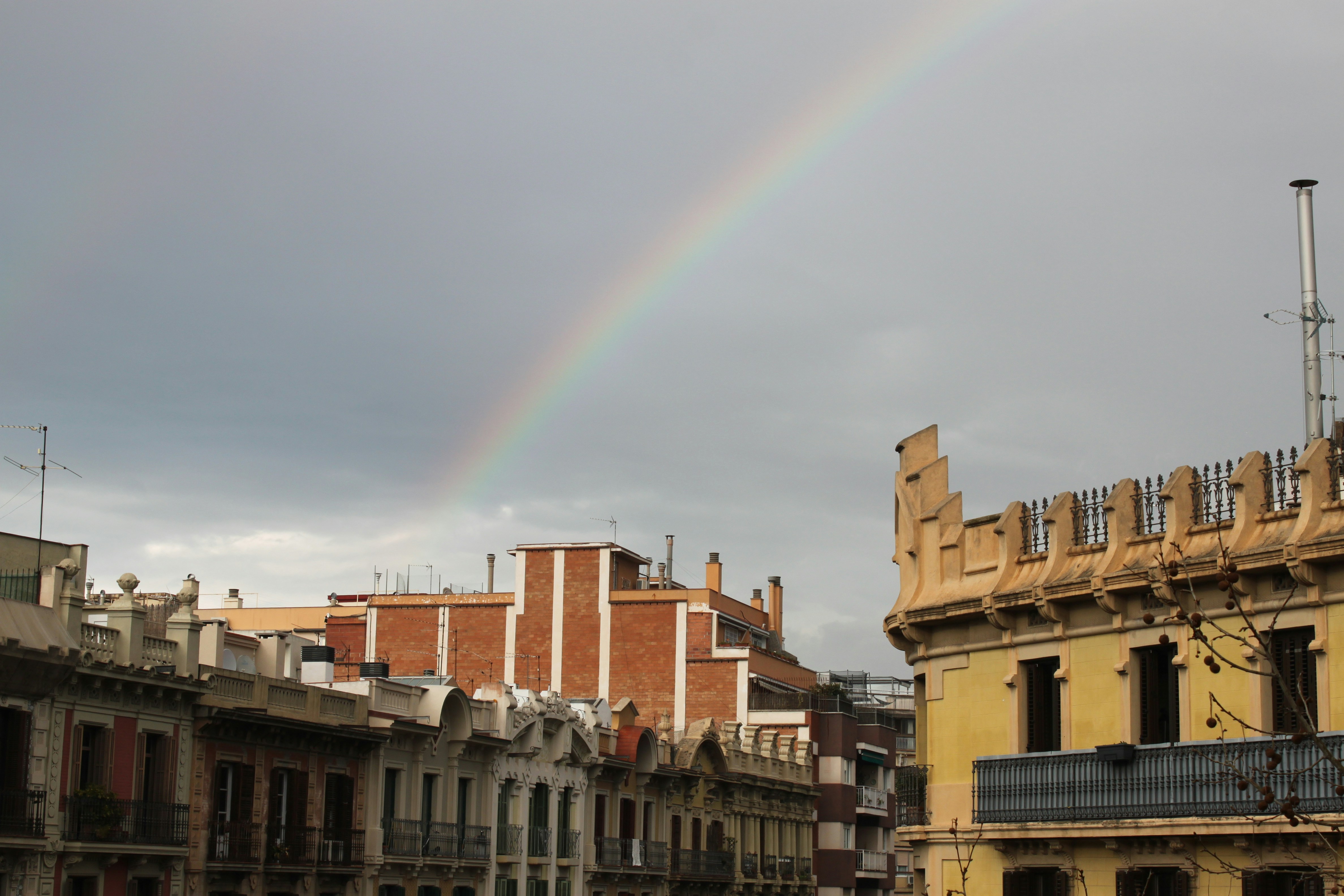 Rainbow Over the City: Rooftops and Brick Facades Under Cloudy Skies
