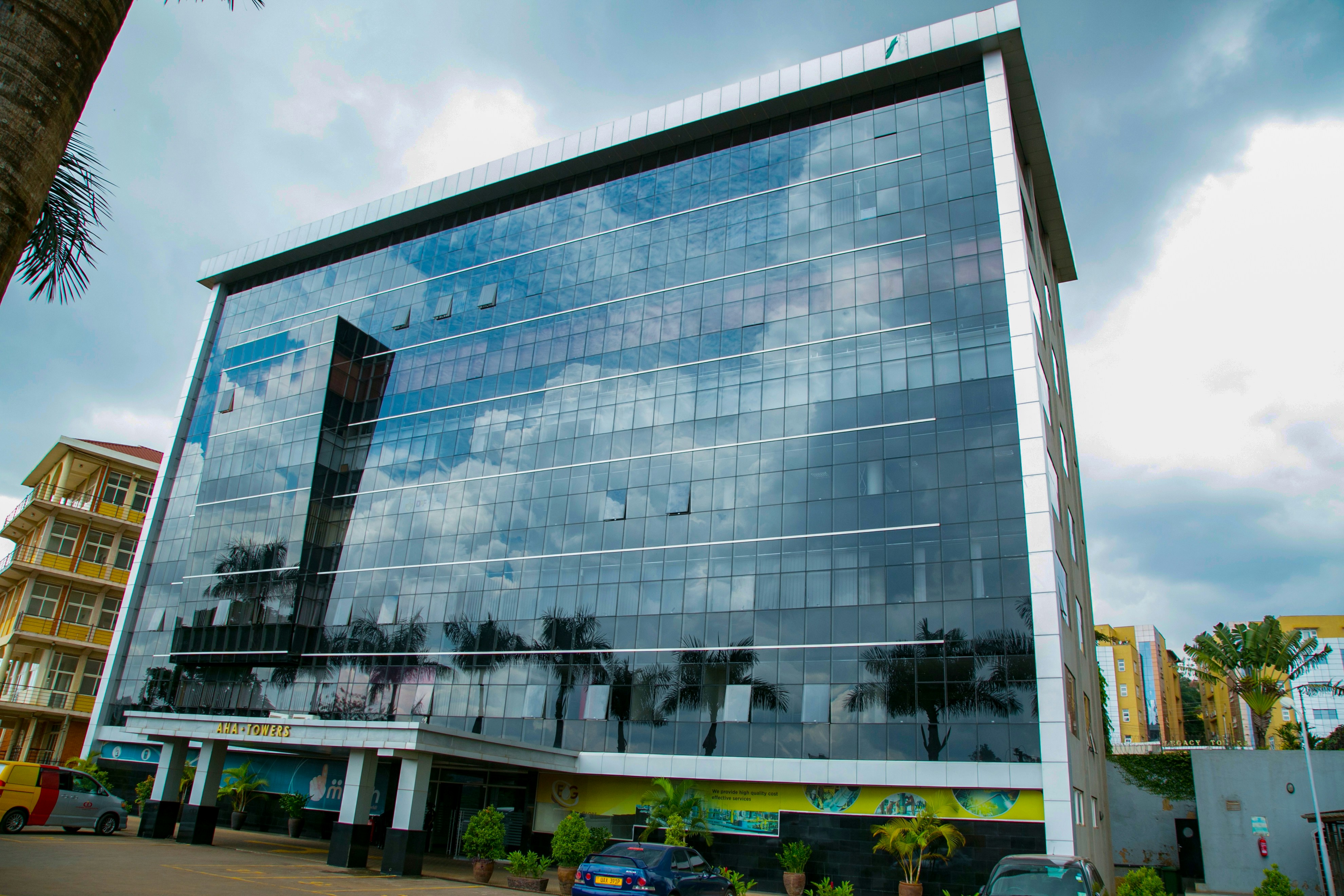 Modern glass building reflecting a cloudy sky and nearby structures.