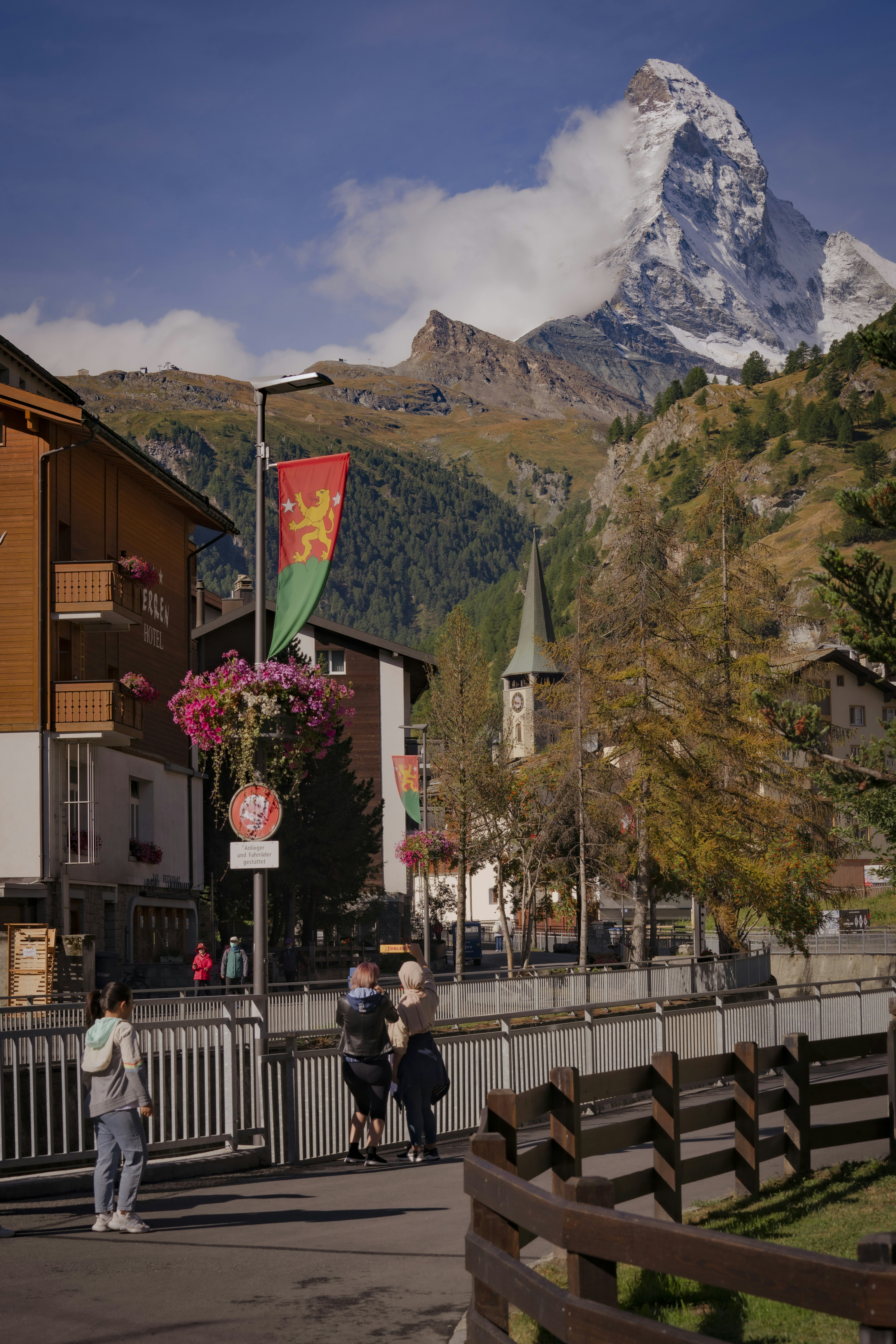 Matterhorn in Focus: A Sunlit Swiss Village Street Framed by Flowers and Flags