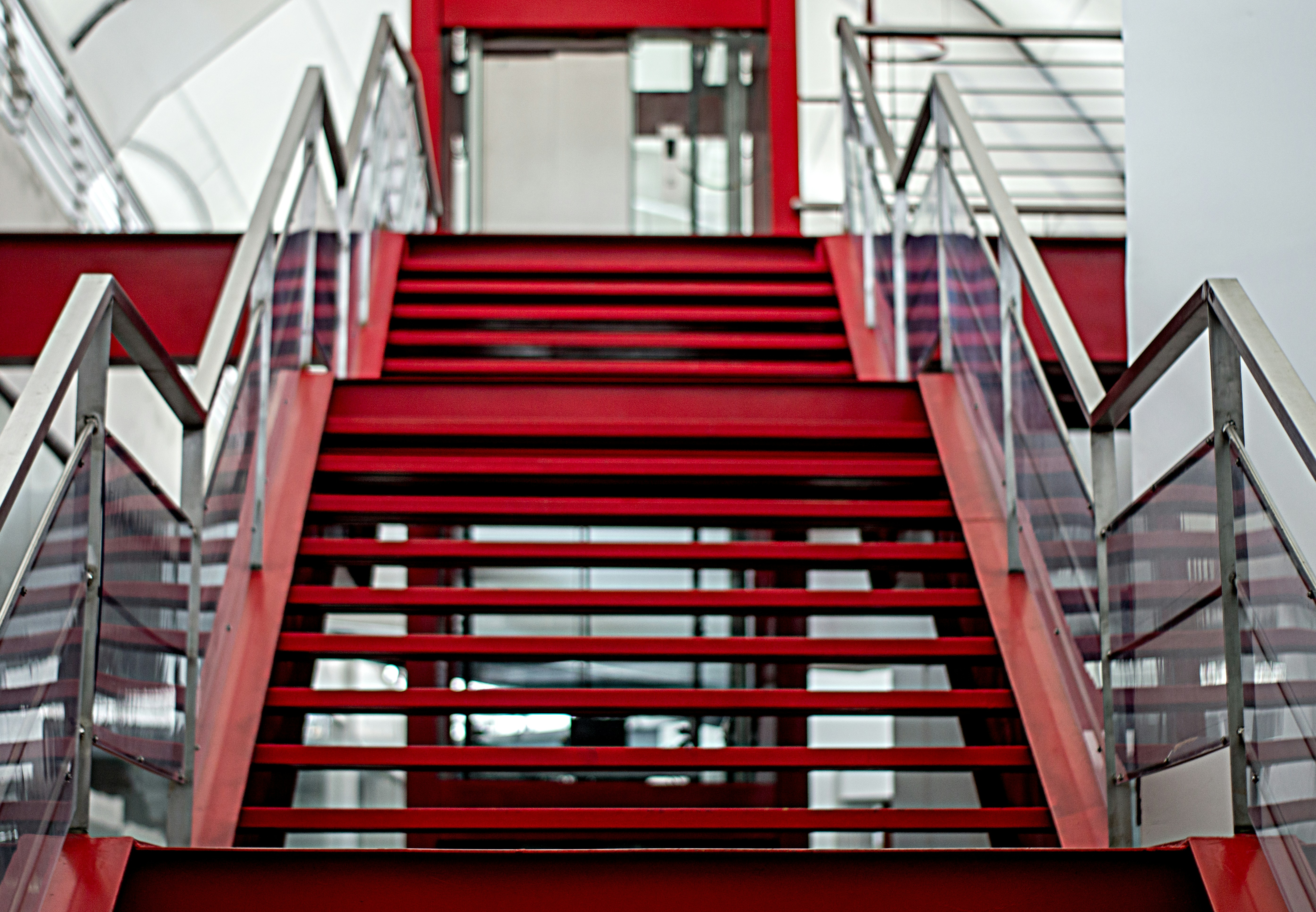 Red staircase with glass railings leading upward in a modern architectural space.