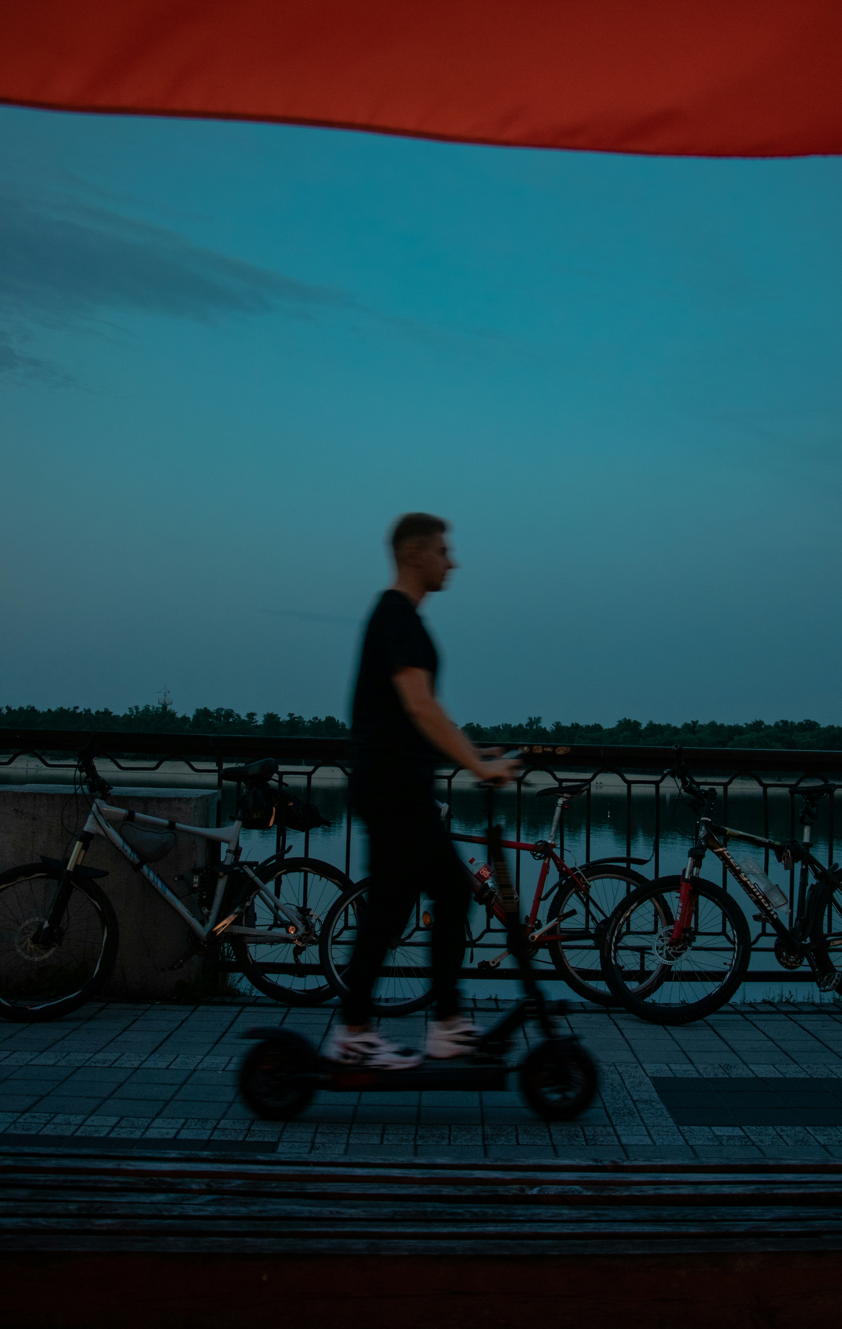 Evening Ride: A lone scooter glides past a row of bicycles by the river