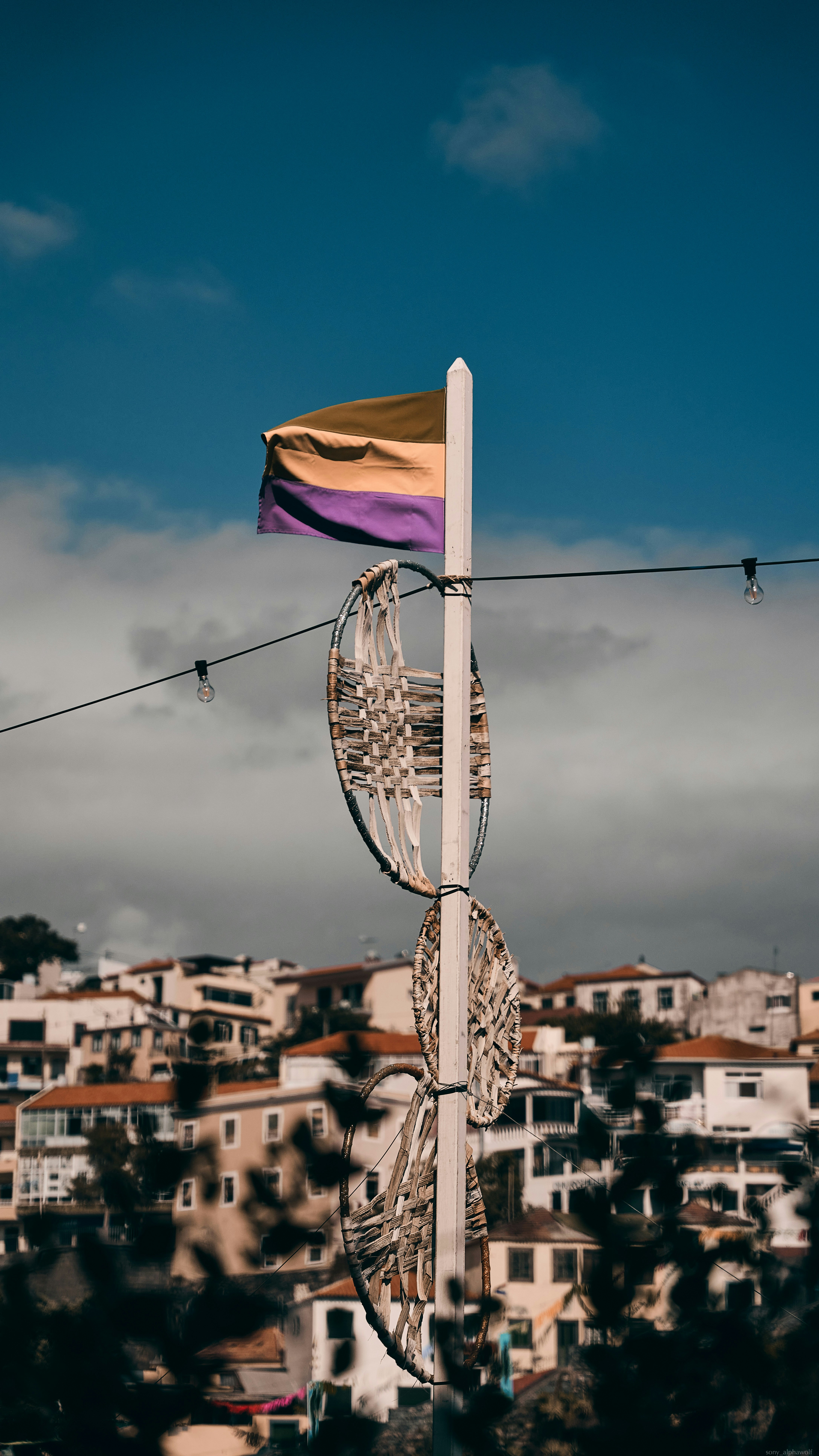 Flagpole Above a Mediterranean Hillside Town with Woven Ornaments and String Lights