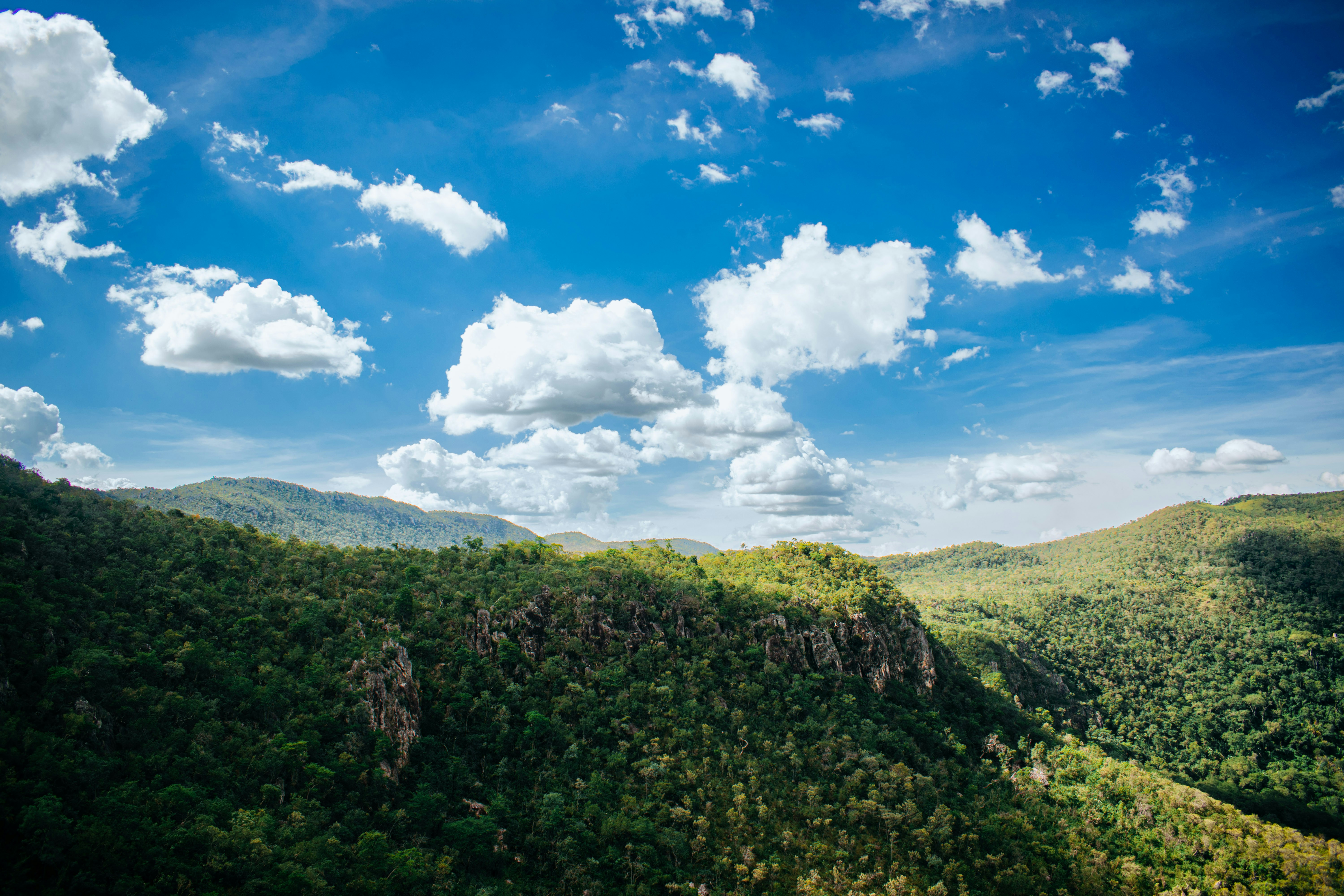 Rolling green hills under a bright blue sky dotted with fluffy clouds.