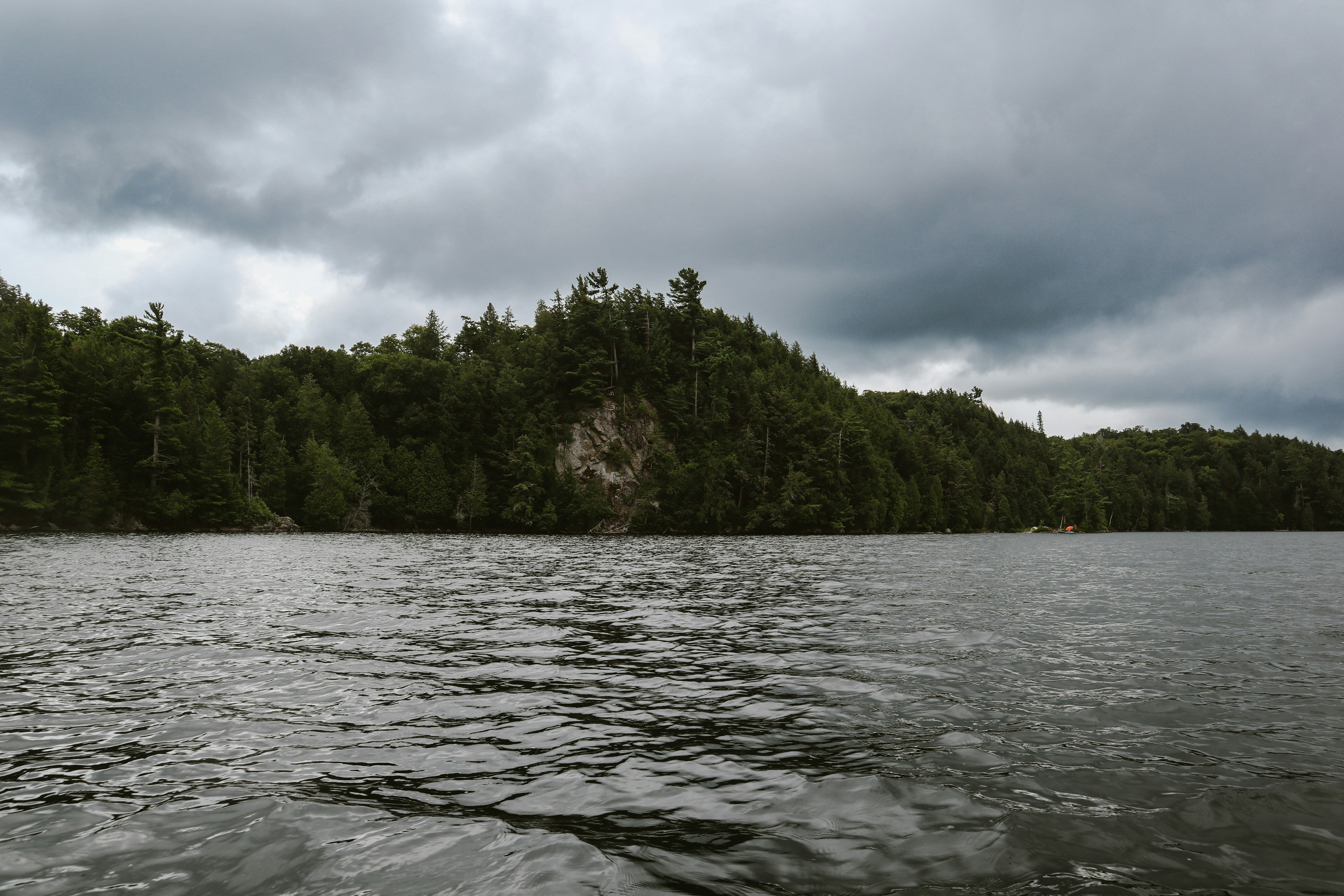 Cloud-laden sky over a forested hillside reflecting on a calm lake.