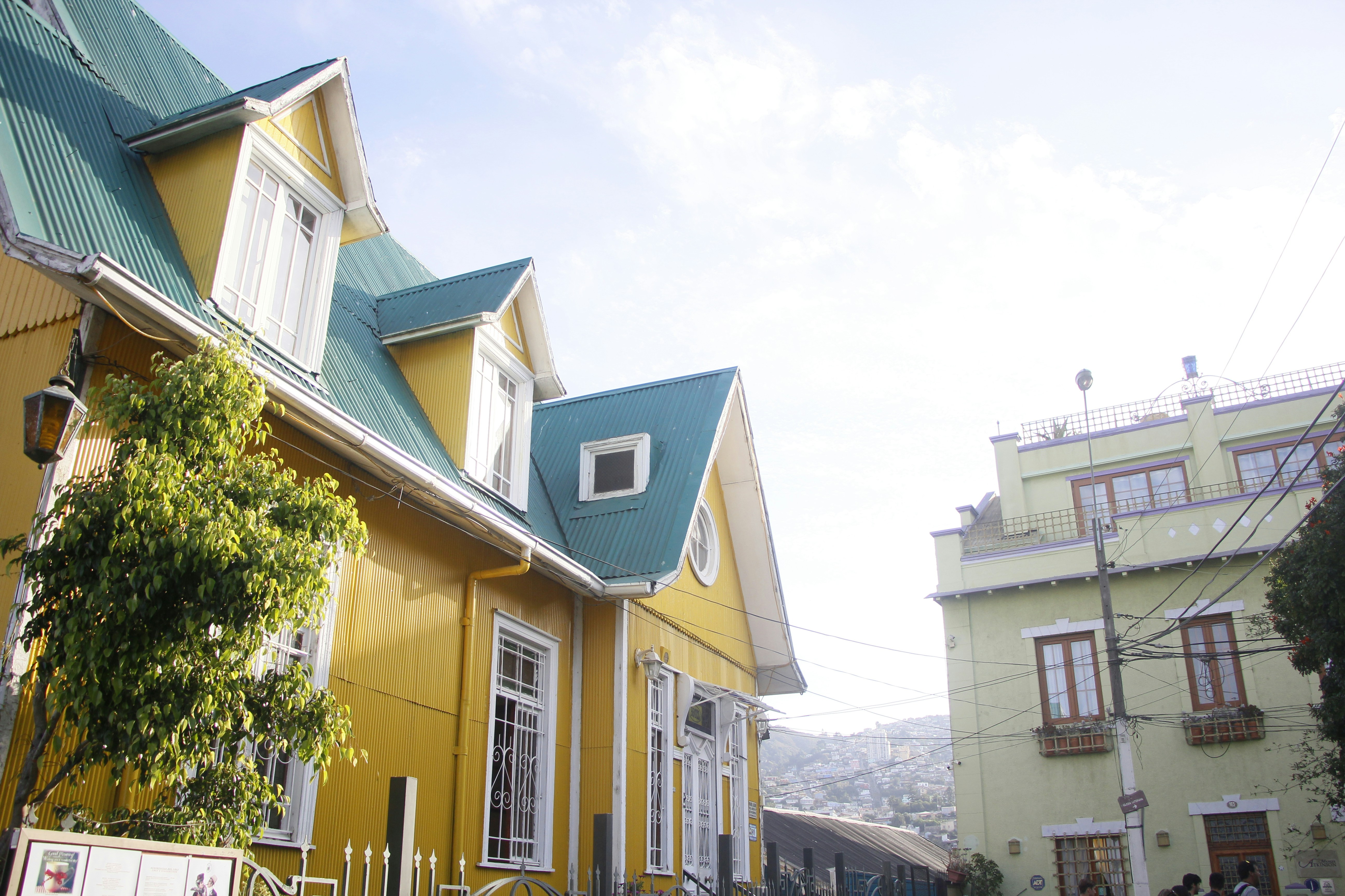 Colorful houses with steep roofs under a bright blue sky, framed by leafy trees.