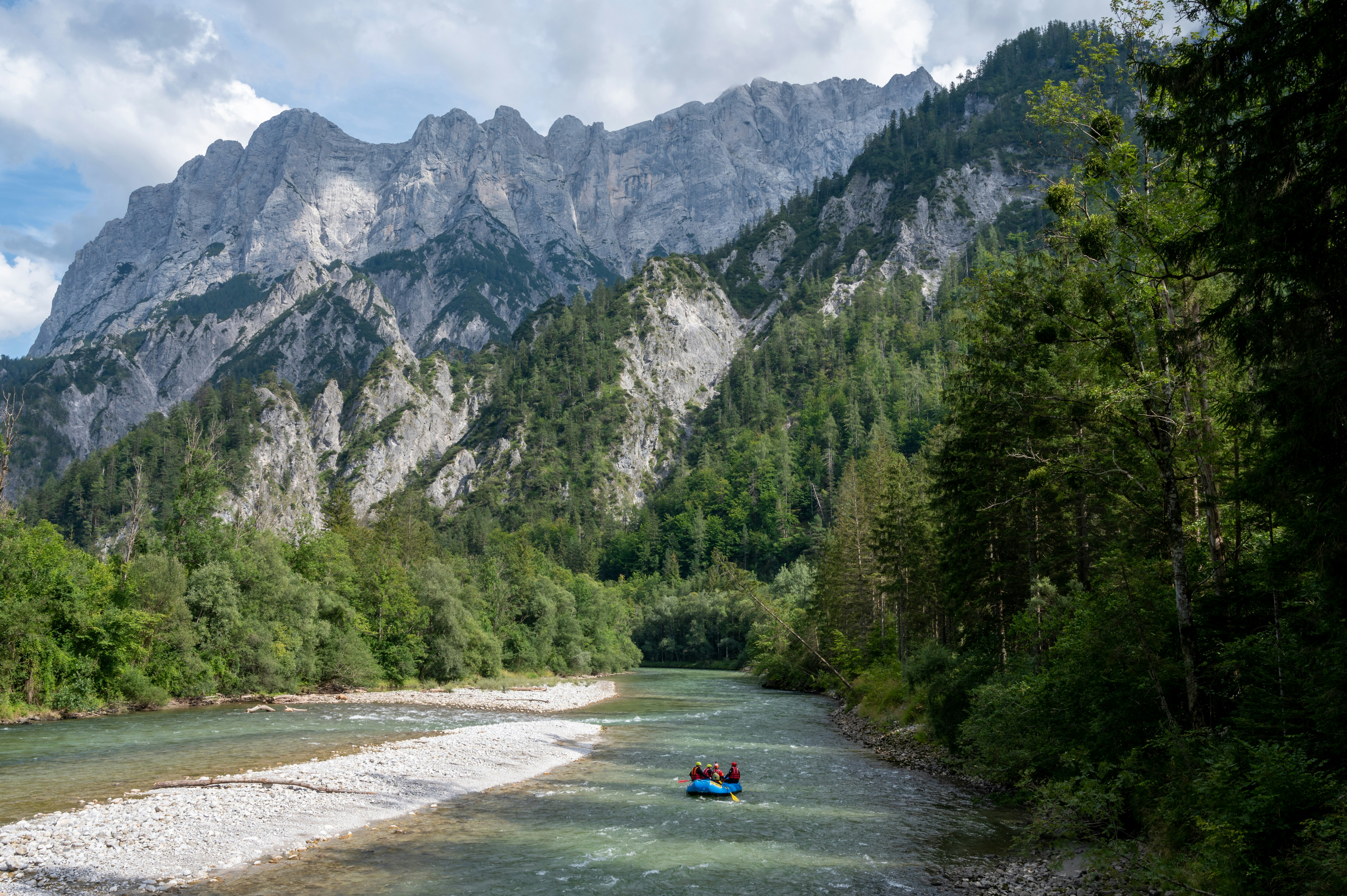 Rafting group navigating a winding river surrounded by majestic mountains and lush forests.