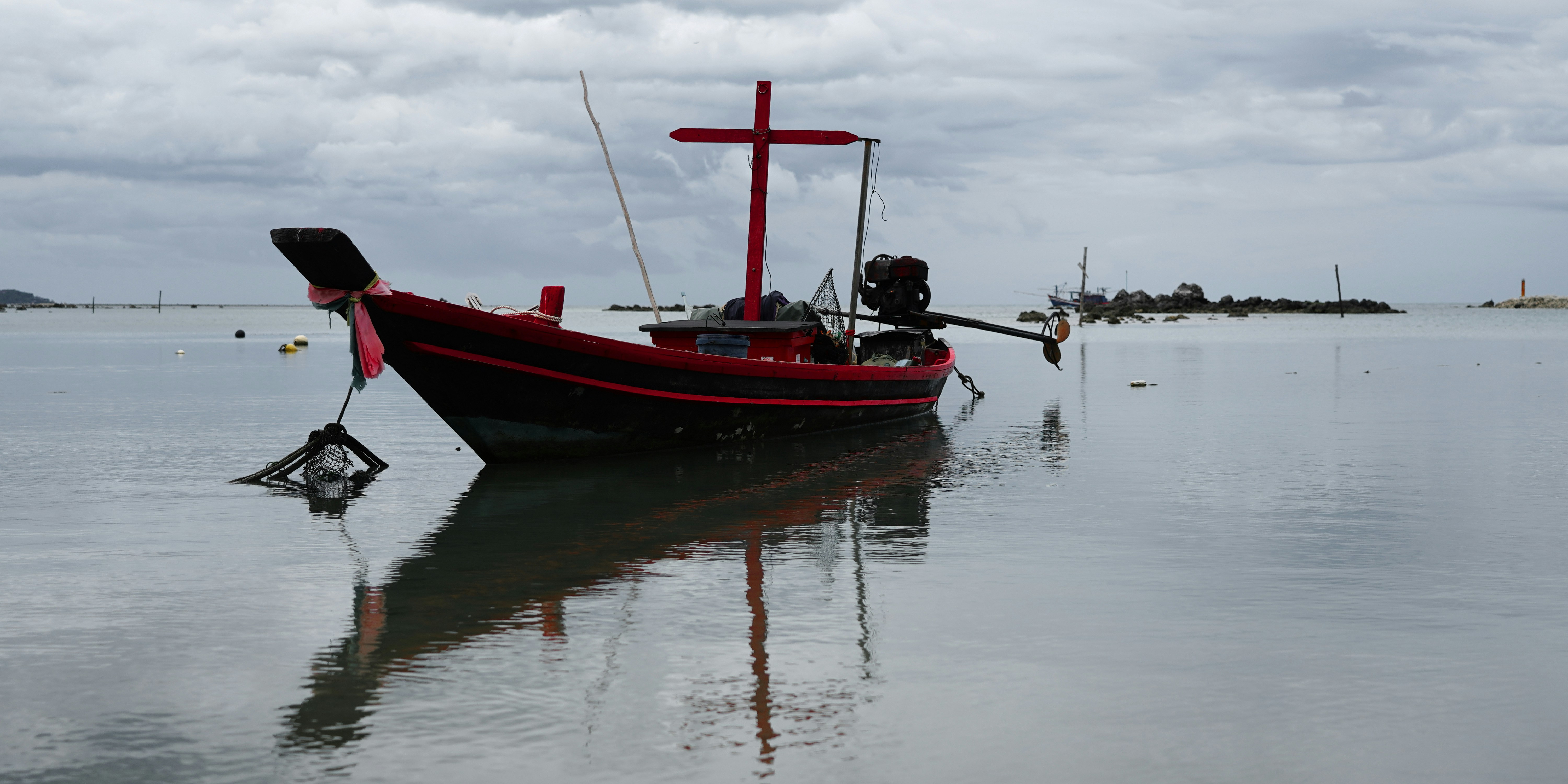 Crimson Vessel on a Glassy Lagoon Beneath Gray Skies