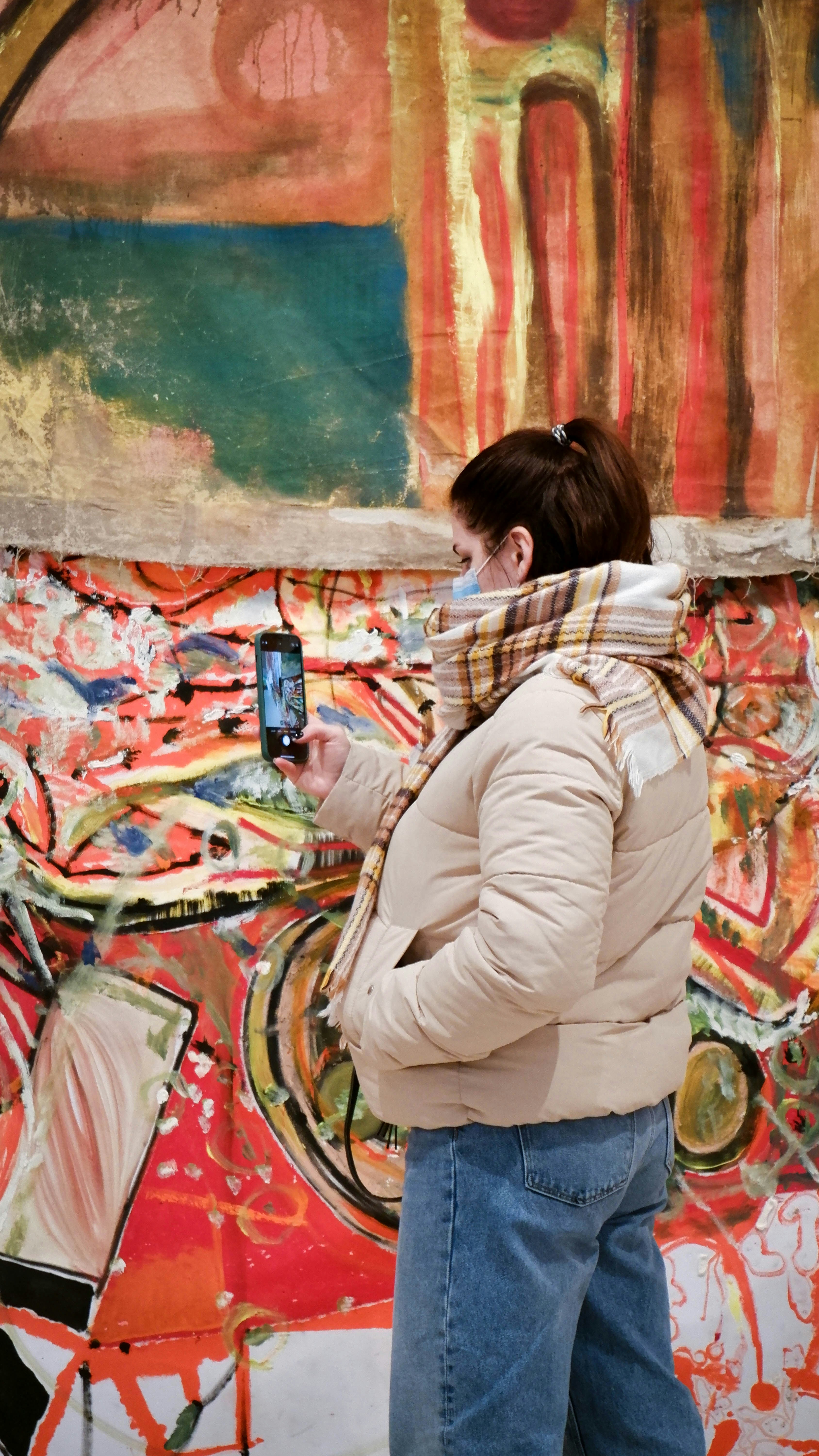 Masked Portrait: A Woman Captures Artful Moments with Her Phone Against a Vivid Graffiti Backdrop