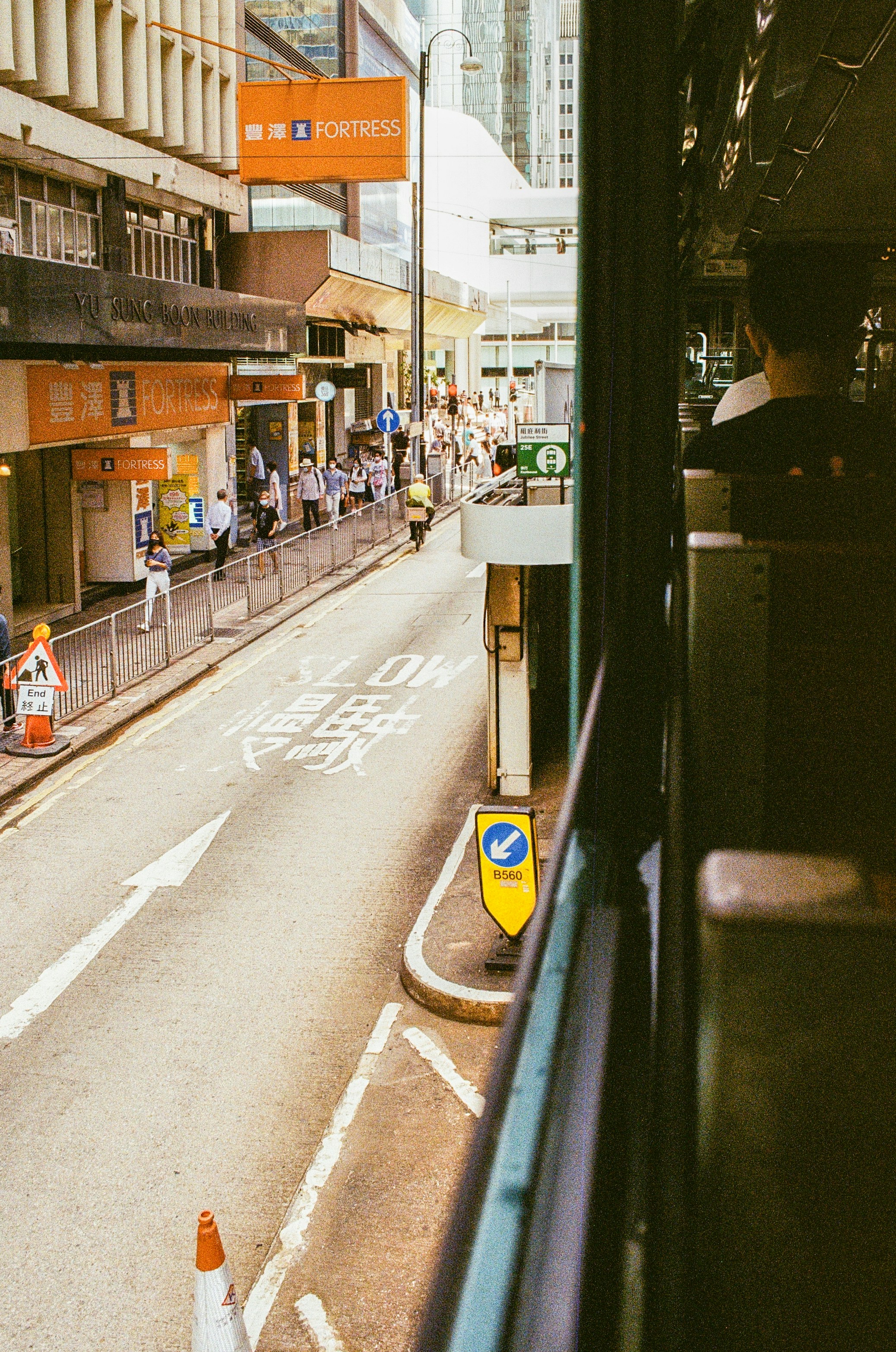 View of a bustling city street from a bus, featuring pedestrians, a cyclist, and vibrant signage.