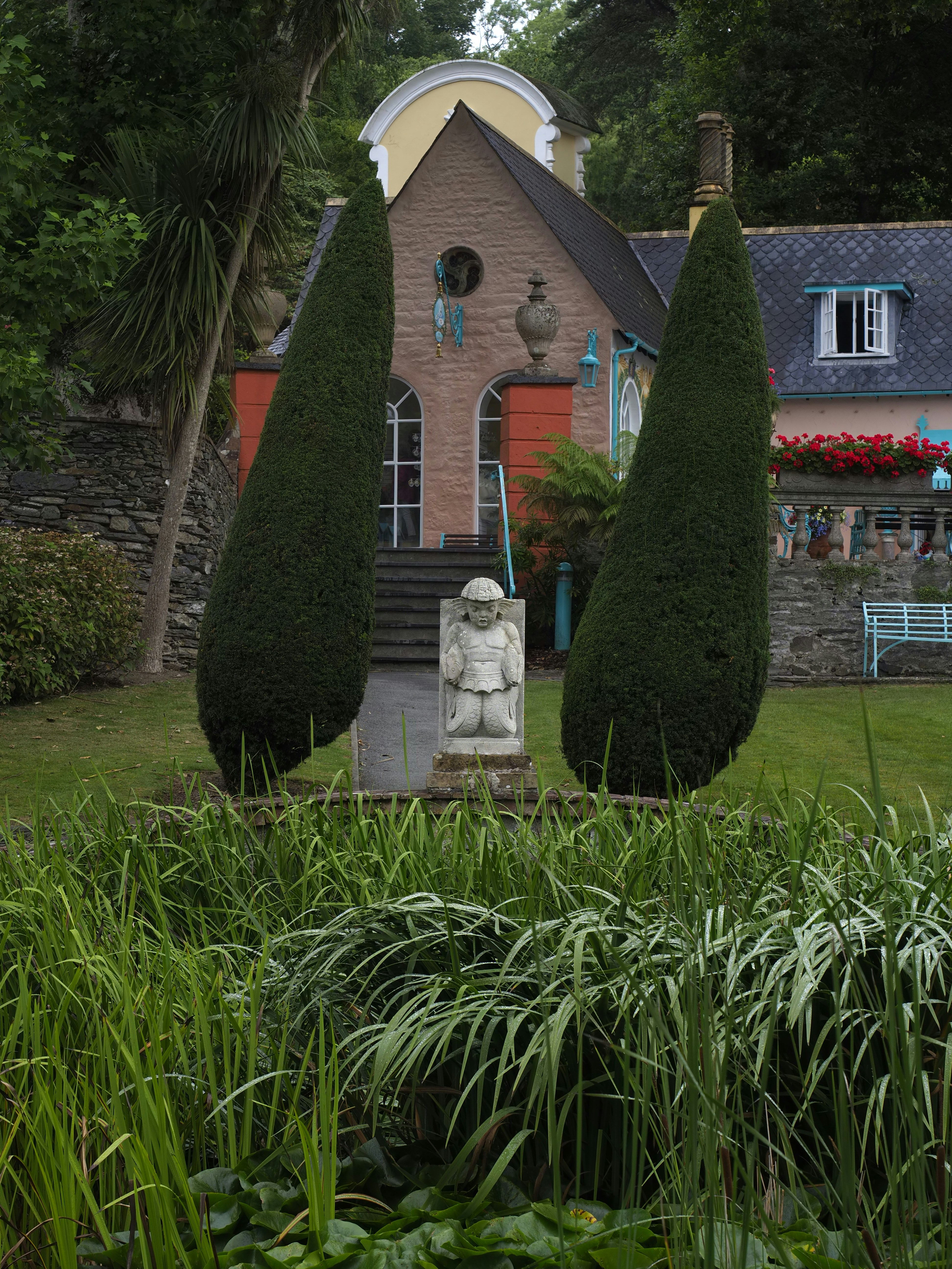 Statue of a small angel overlooking a pond filled with greenery