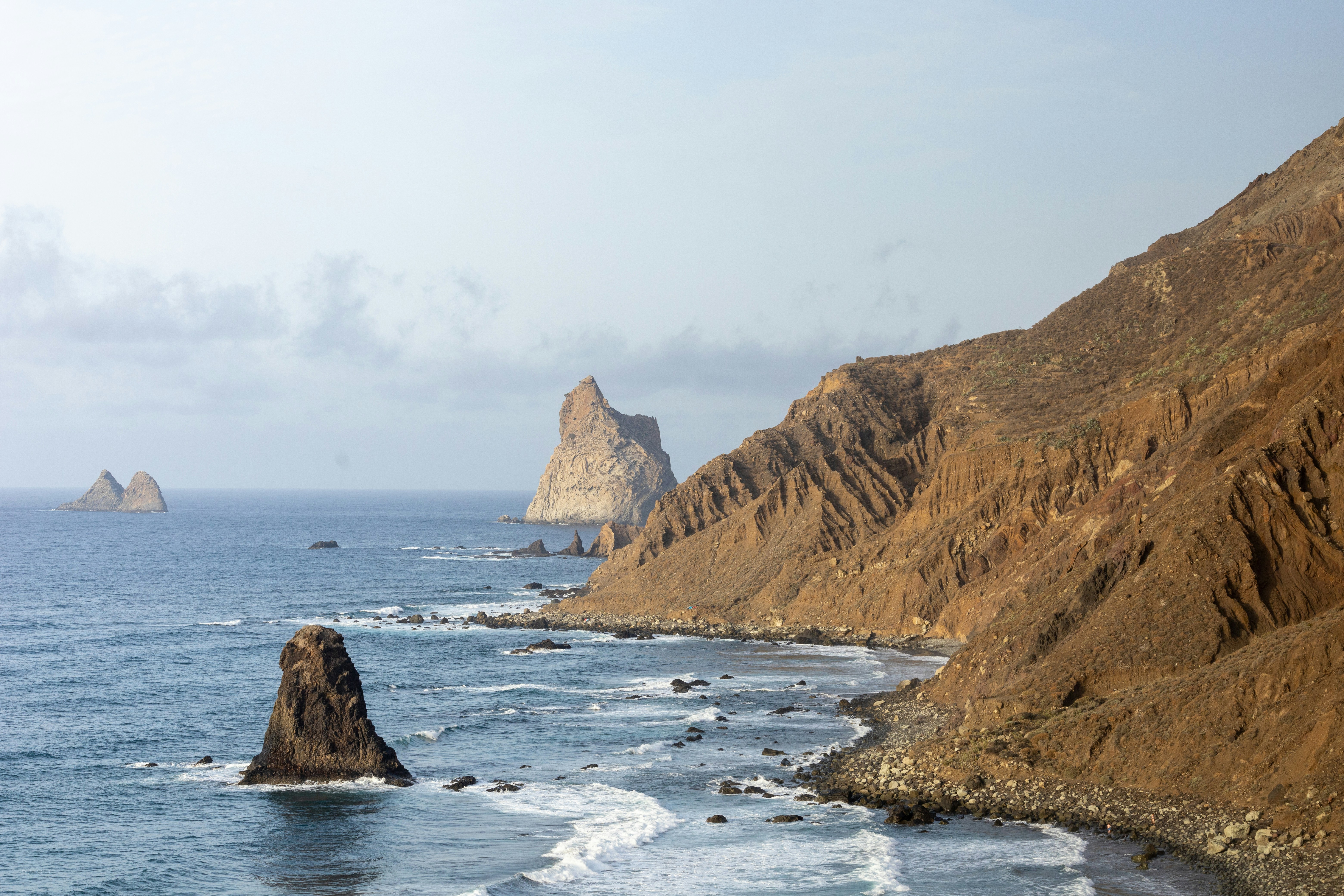 A rocky beach with a body of water and a large rock formation photo ...