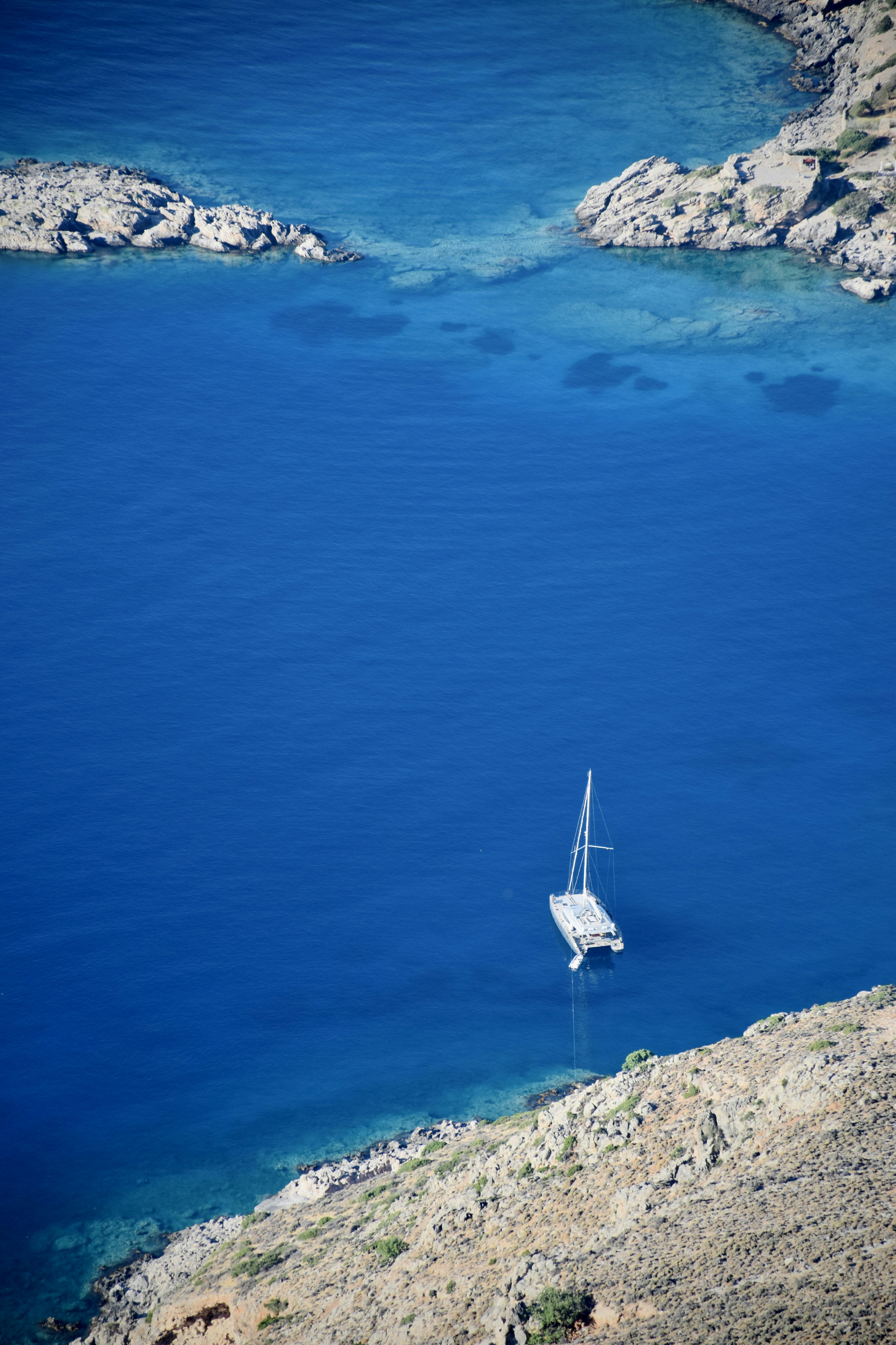 A solitary sailboat anchored in tranquil azure waters, surrounded by rocky shores and vibrant marine hues.