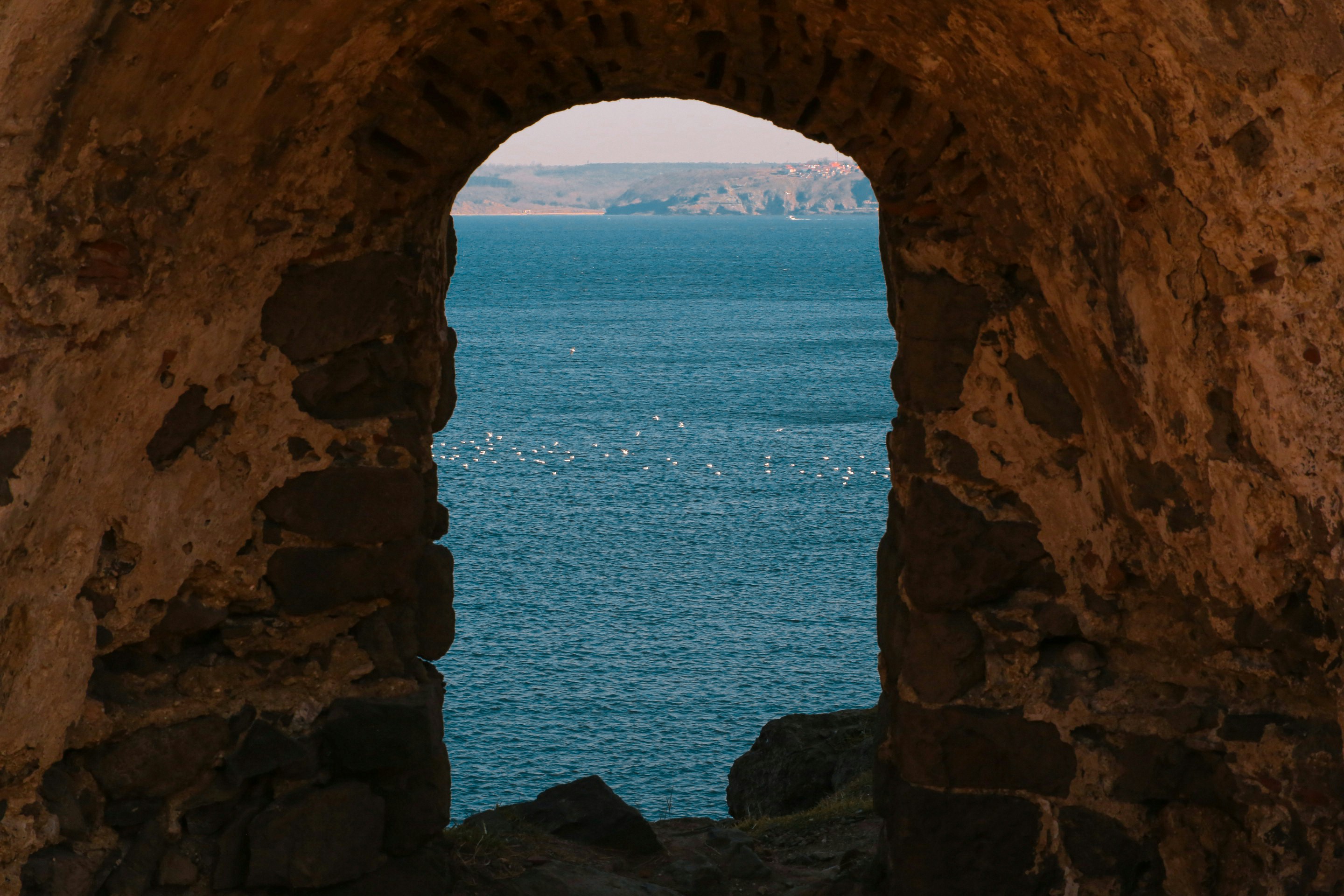 View of a tranquil sea framed by an archway of weathered stone, highlighting the contrast between the rugged structure and the calm water beyond.