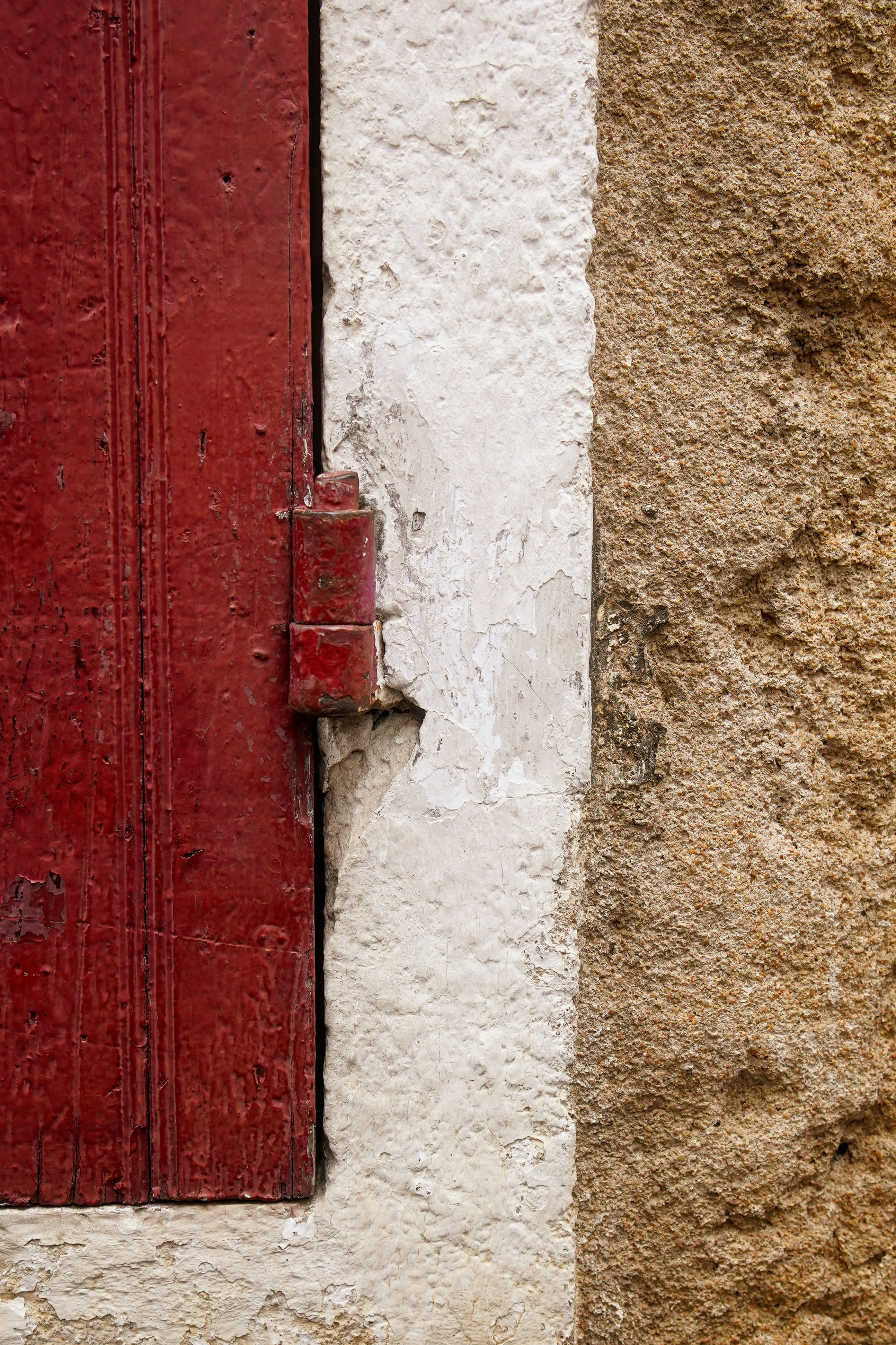 Crimson hinge anchoring a weathered seam between plaster and stone