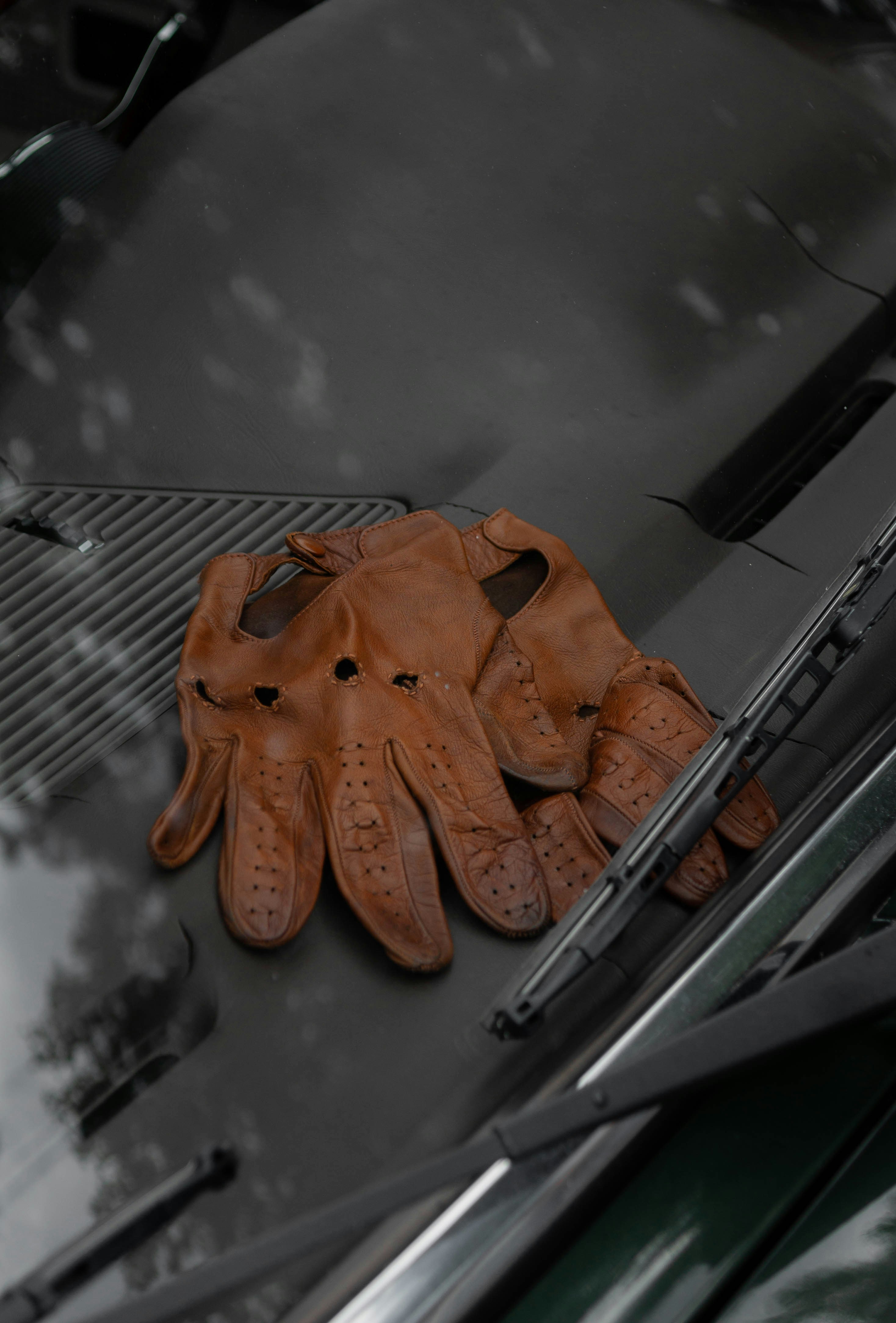 Brown leather driving gloves resting on a car hood, showcasing their intricate design and craftsmanship.