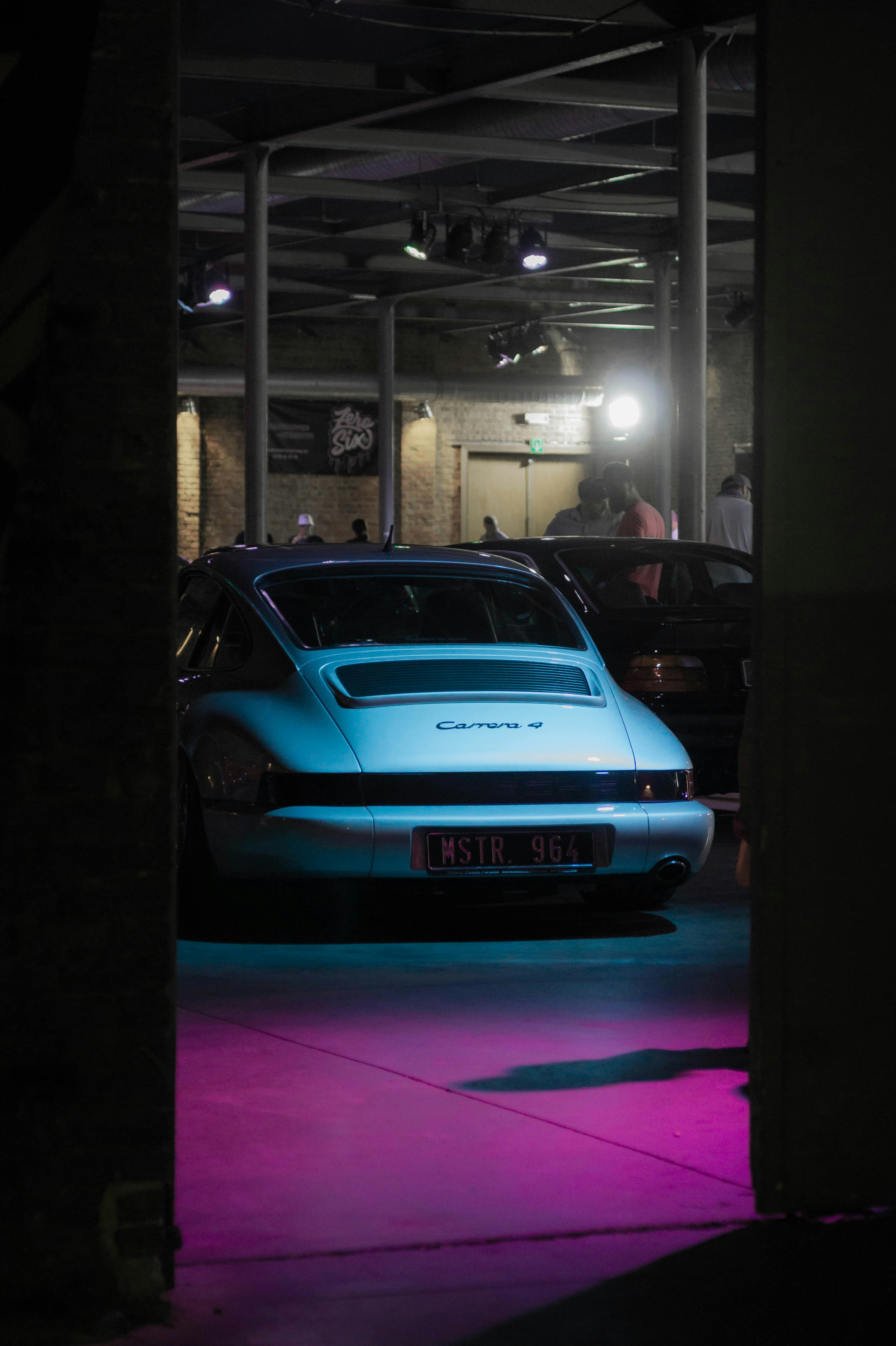 Blue Porsche 911 rear view in a dim, neon-lit showroom with brick walls.